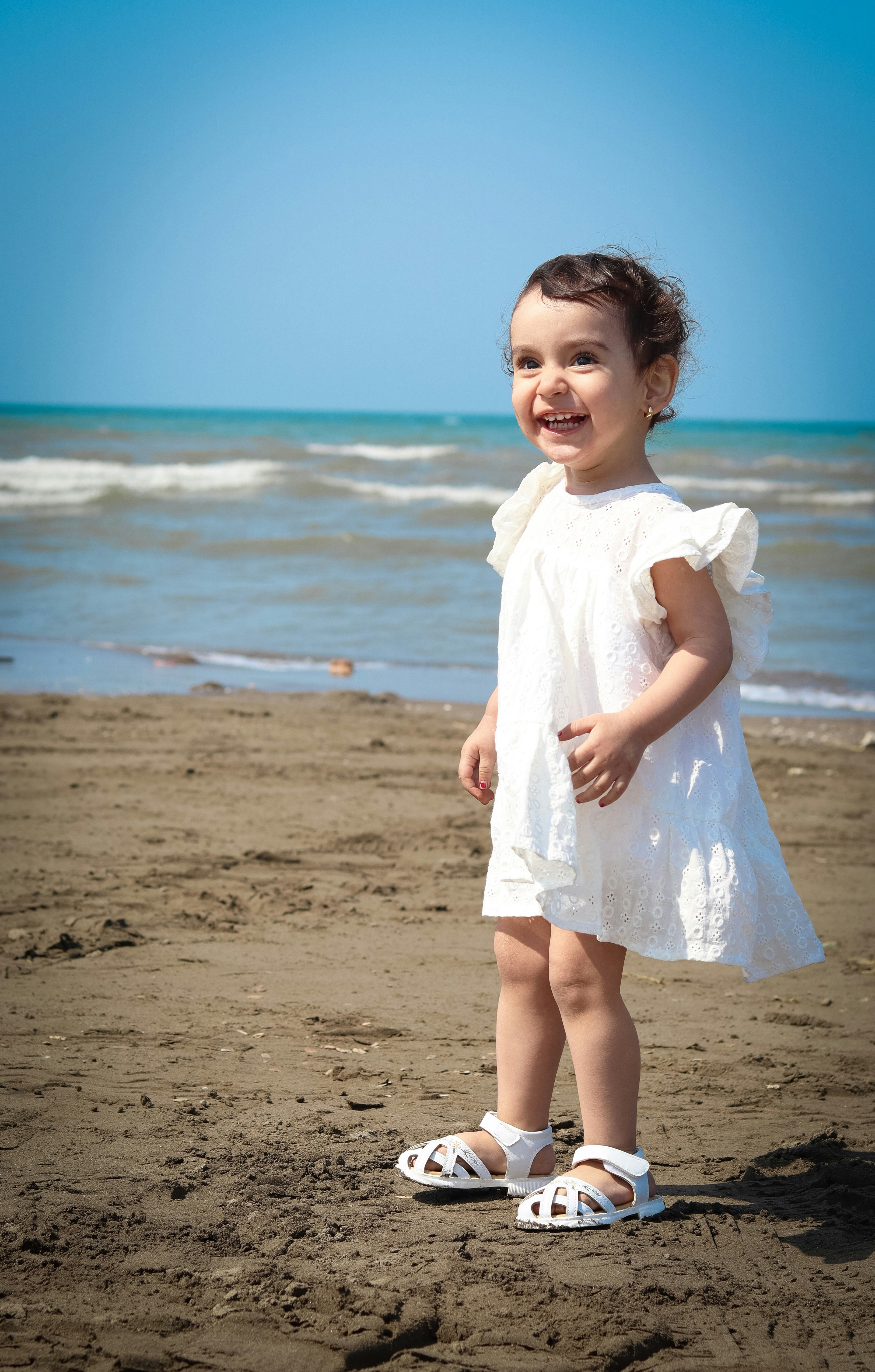 Joyful Beach Smile: A Little Girl in White on Sunlit Sand