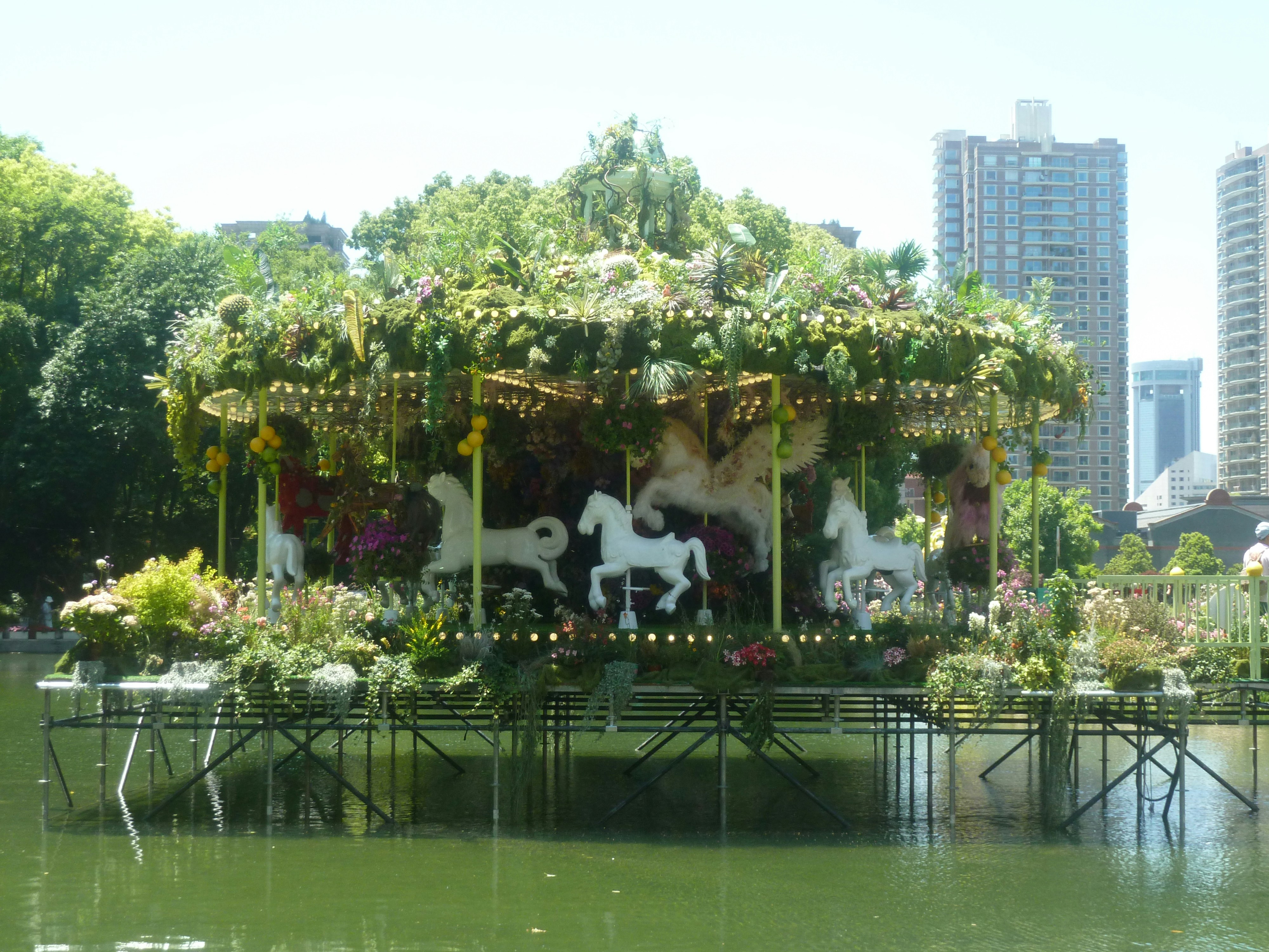 A beautiful floral carousel floats on water with city buildings.