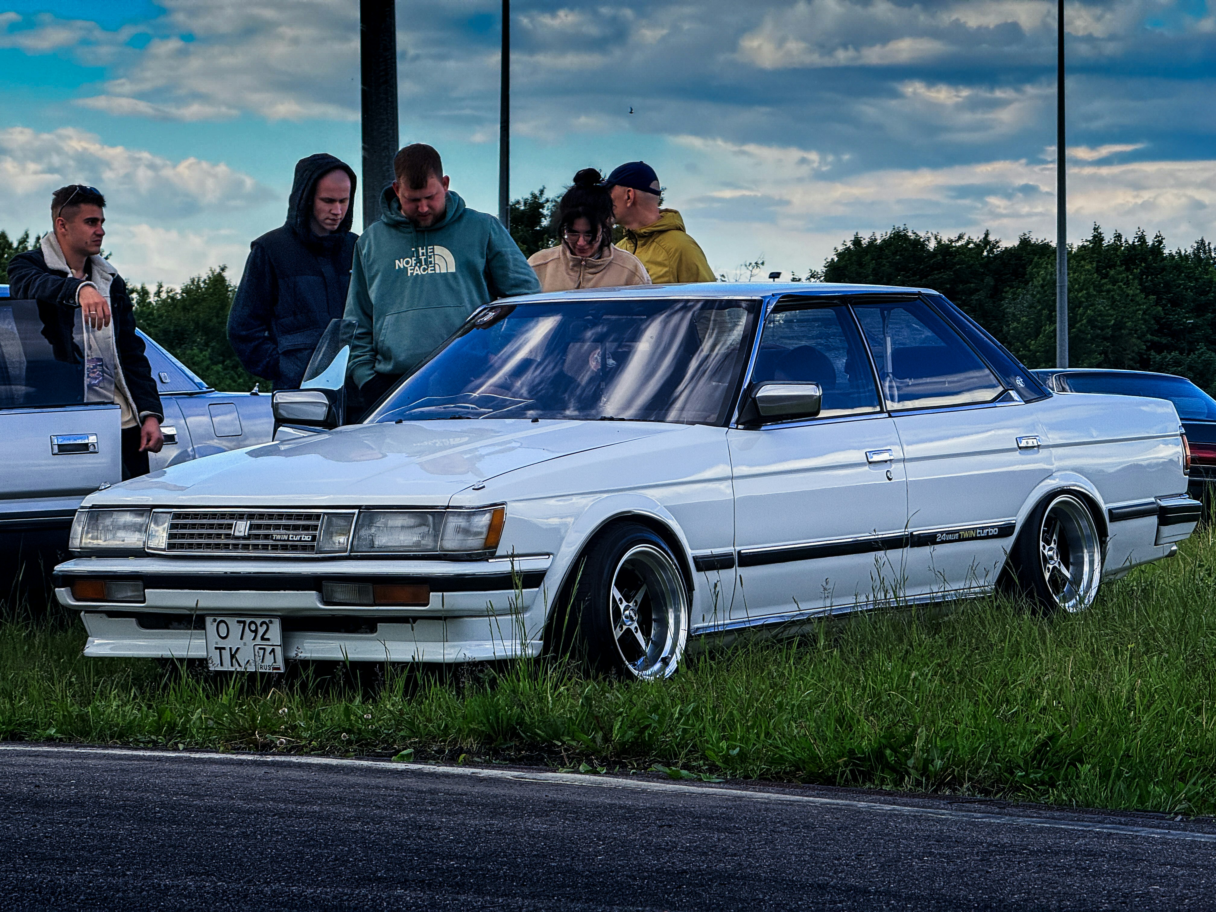 Vintage sedan, modern observers: a roadside car meet by the fields
