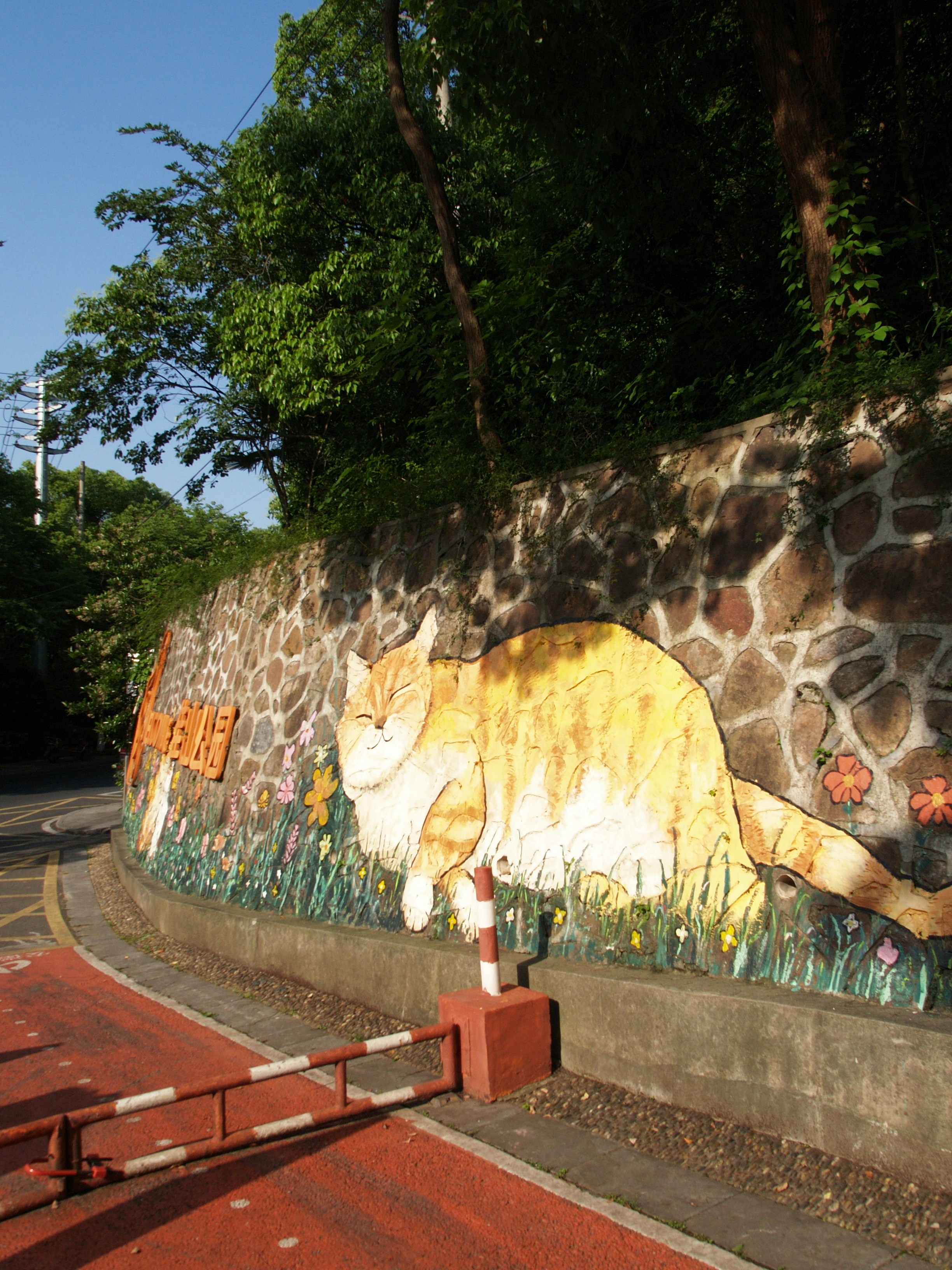 Sunlit mural of a sleeping cat along a stone wall beside a winding road