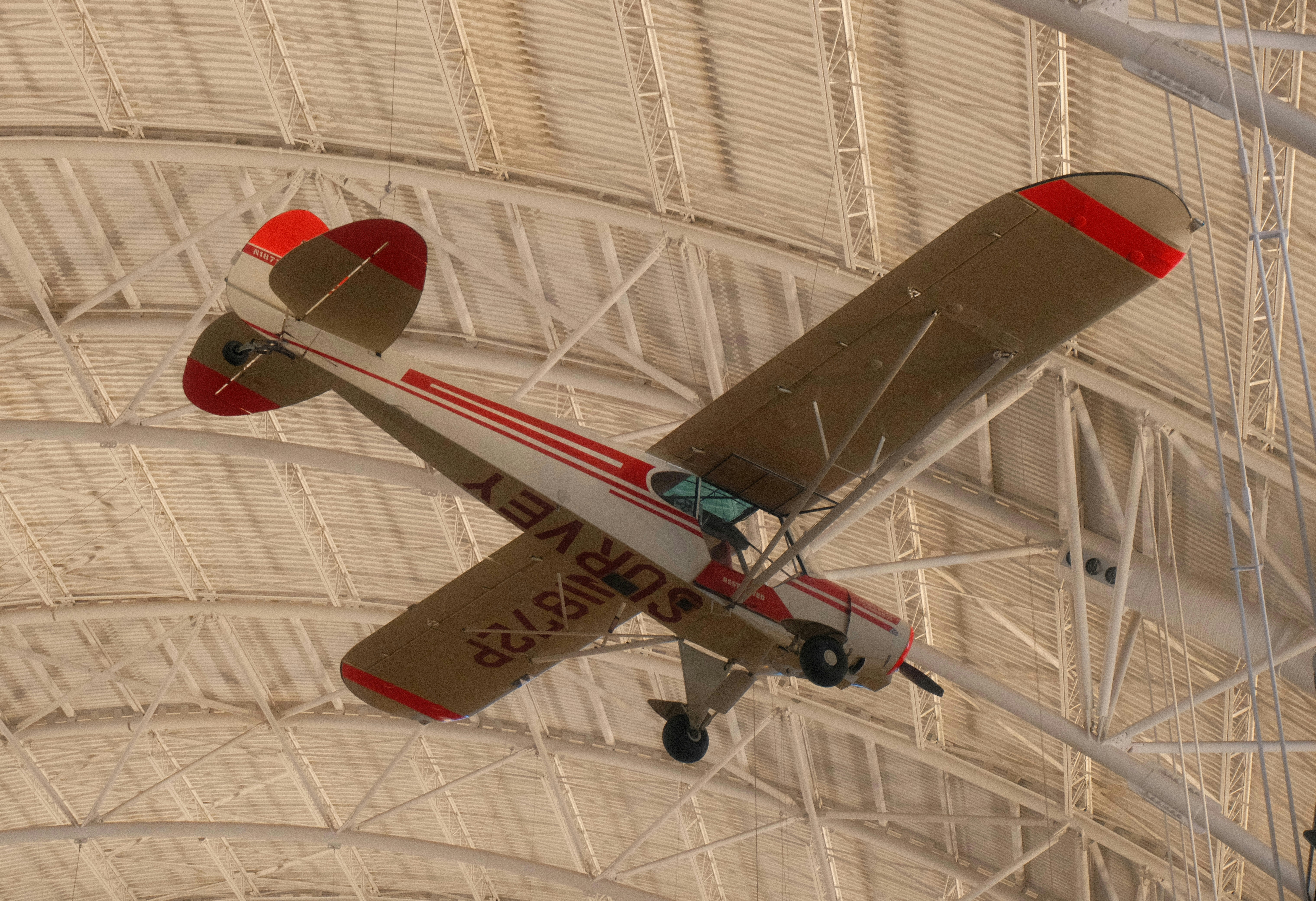 A small vintage airplane suspended from a large arched ceiling.