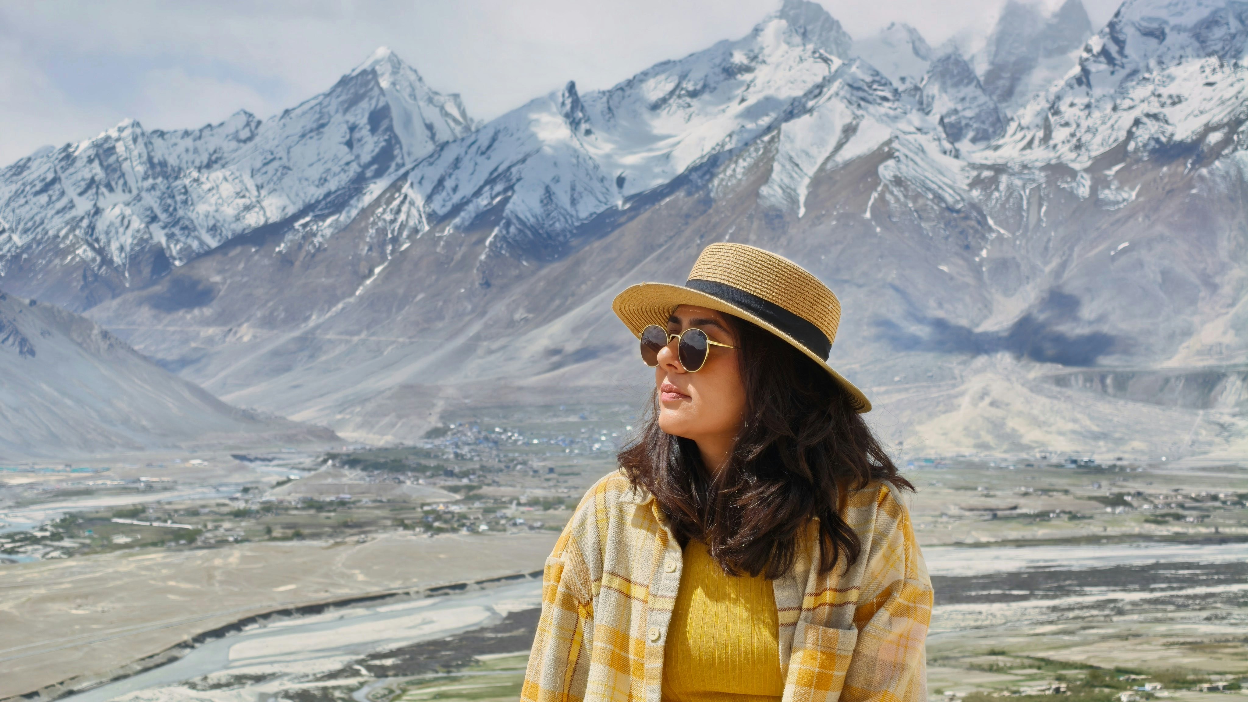 Woman in hat and sunglasses against snowy mountain landscape.