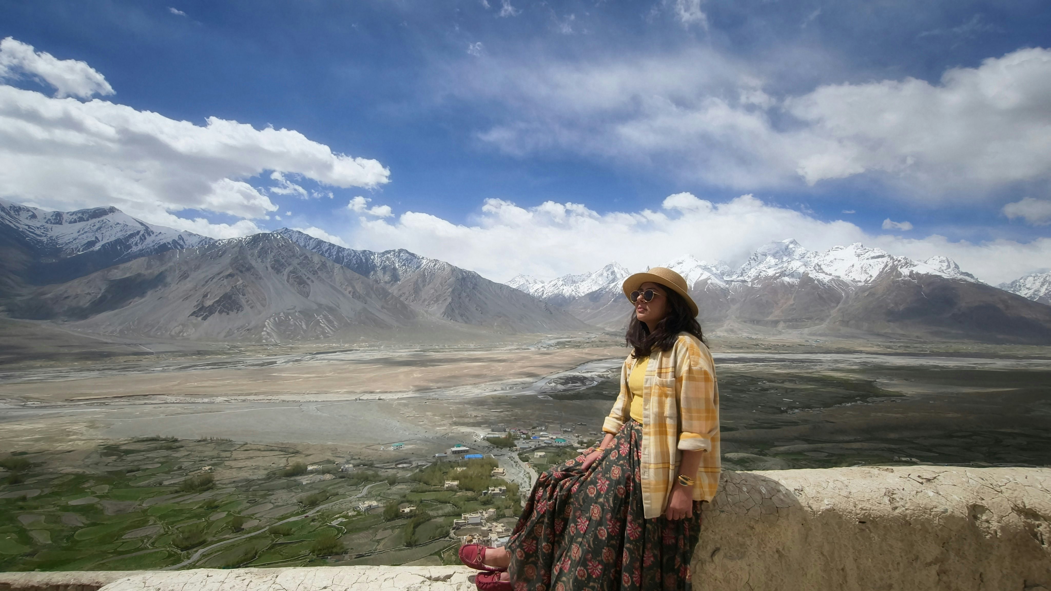 Woman in a Yellow Plaid Shirt and Wide-Brim Hat overlooking a valley with snow-capped mountains