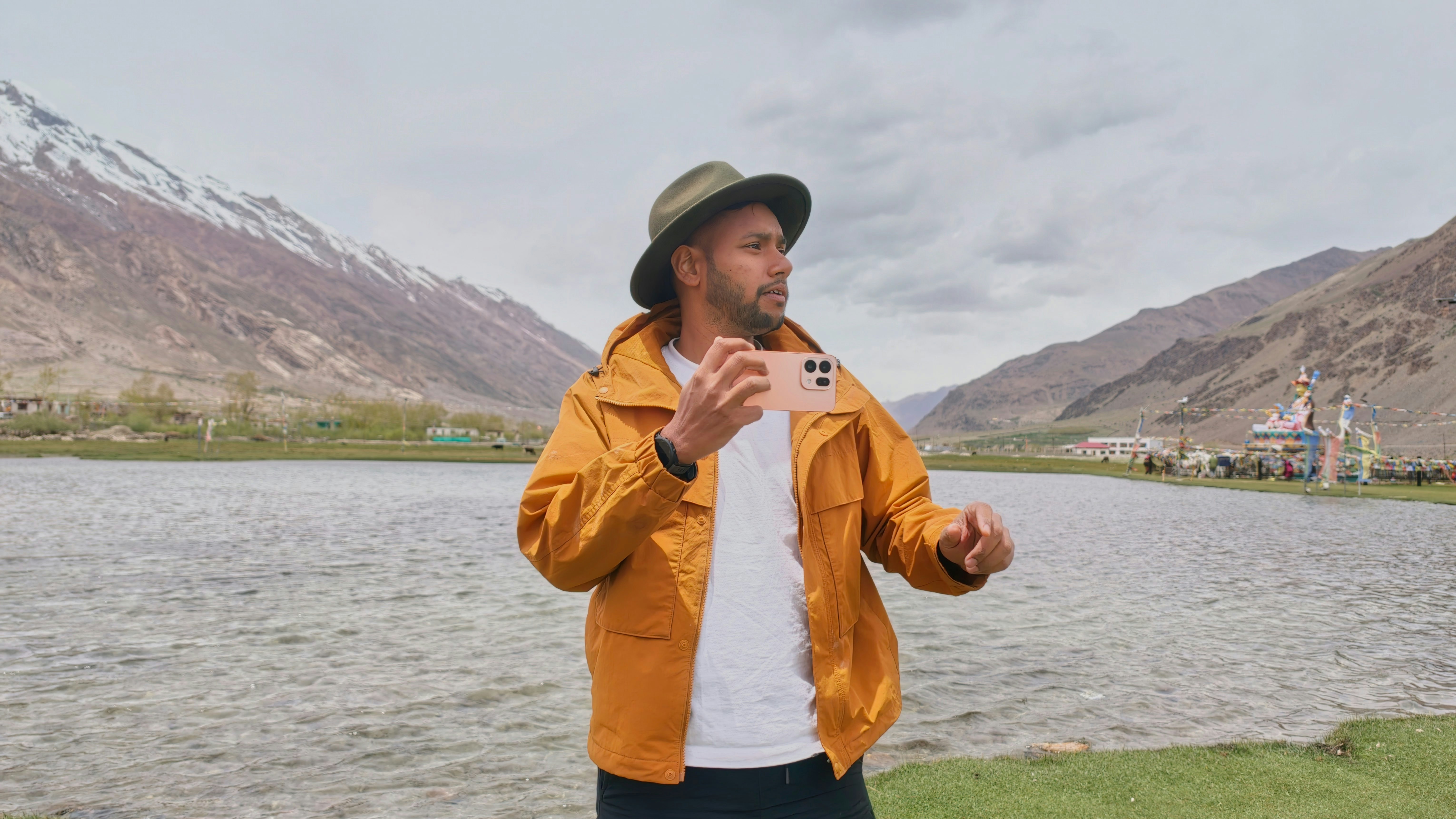 Man in yellow jacket holding phone by mountain lake.