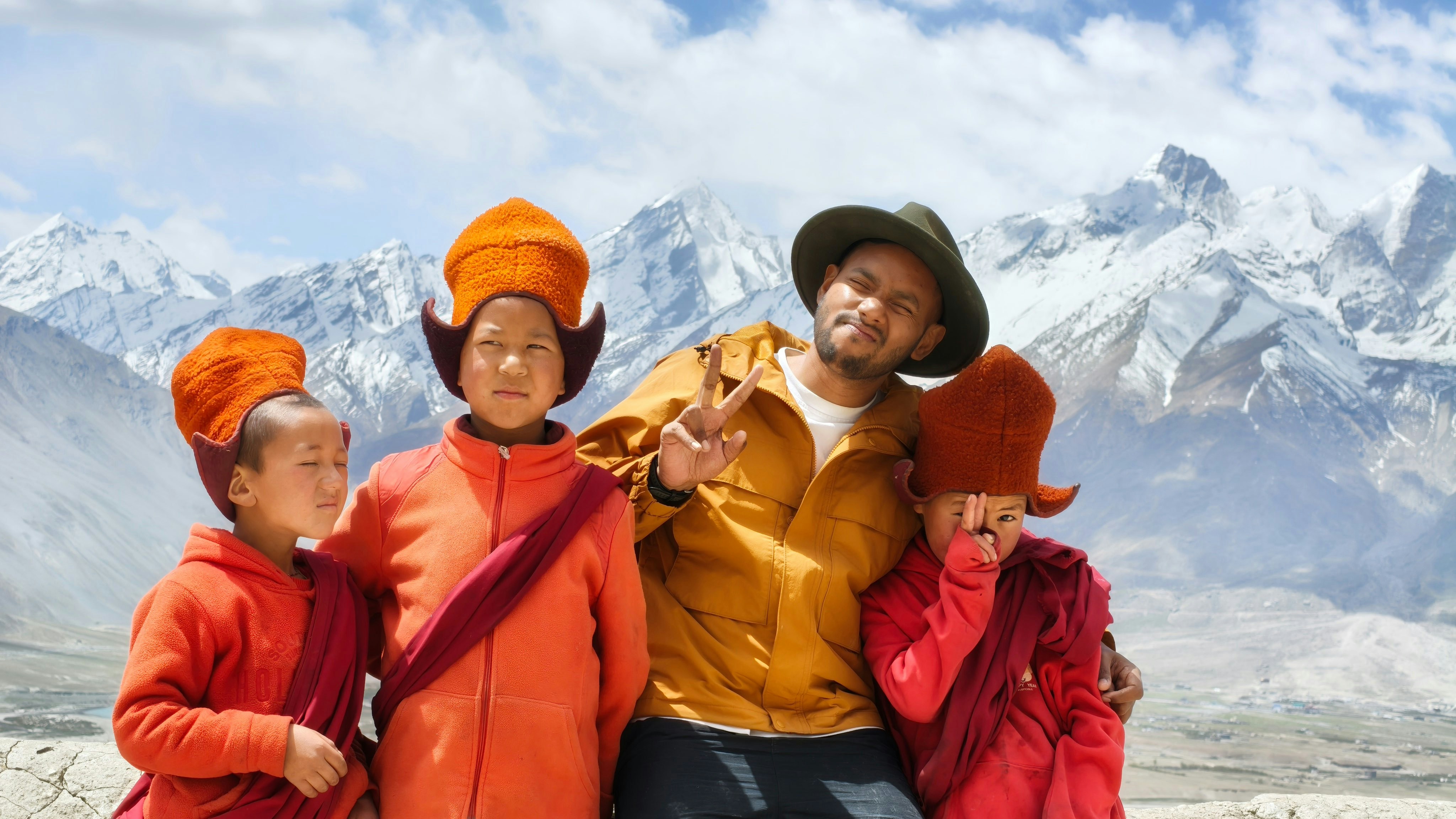 Man making peace sign with three monks and snowy mountains.