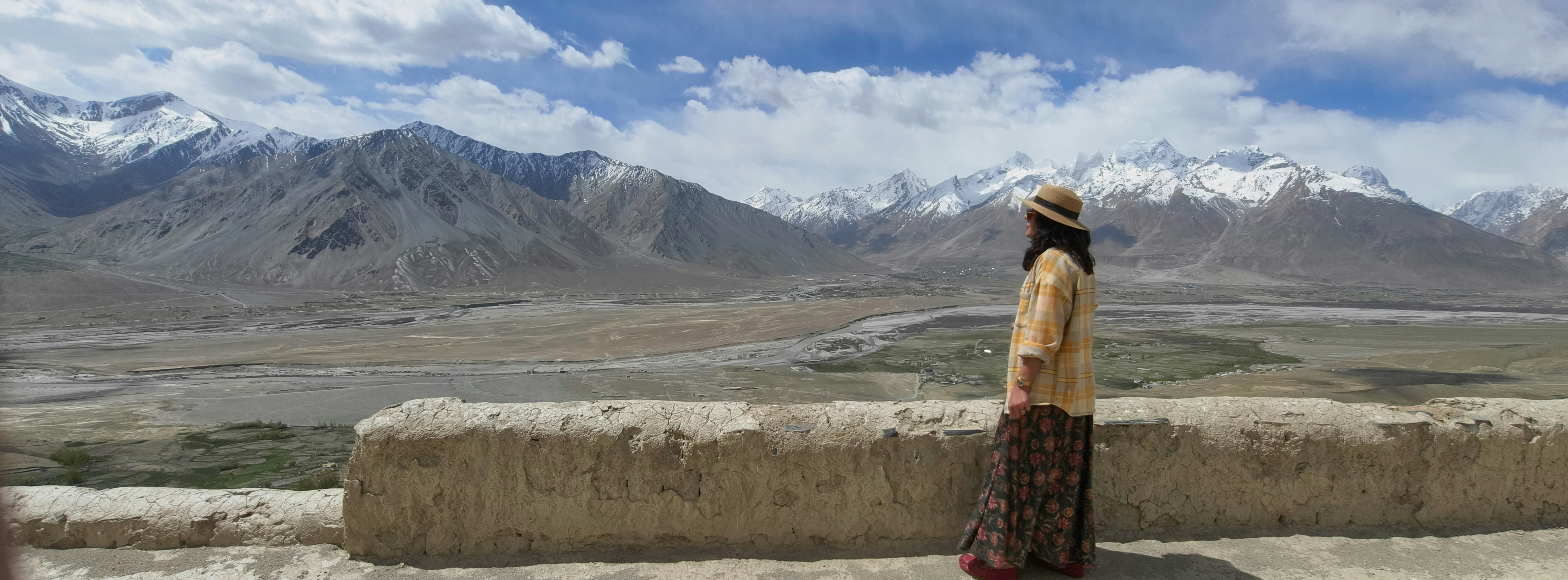 Woman in a mustard top gazes toward snow-capped peaks across a barren valley
