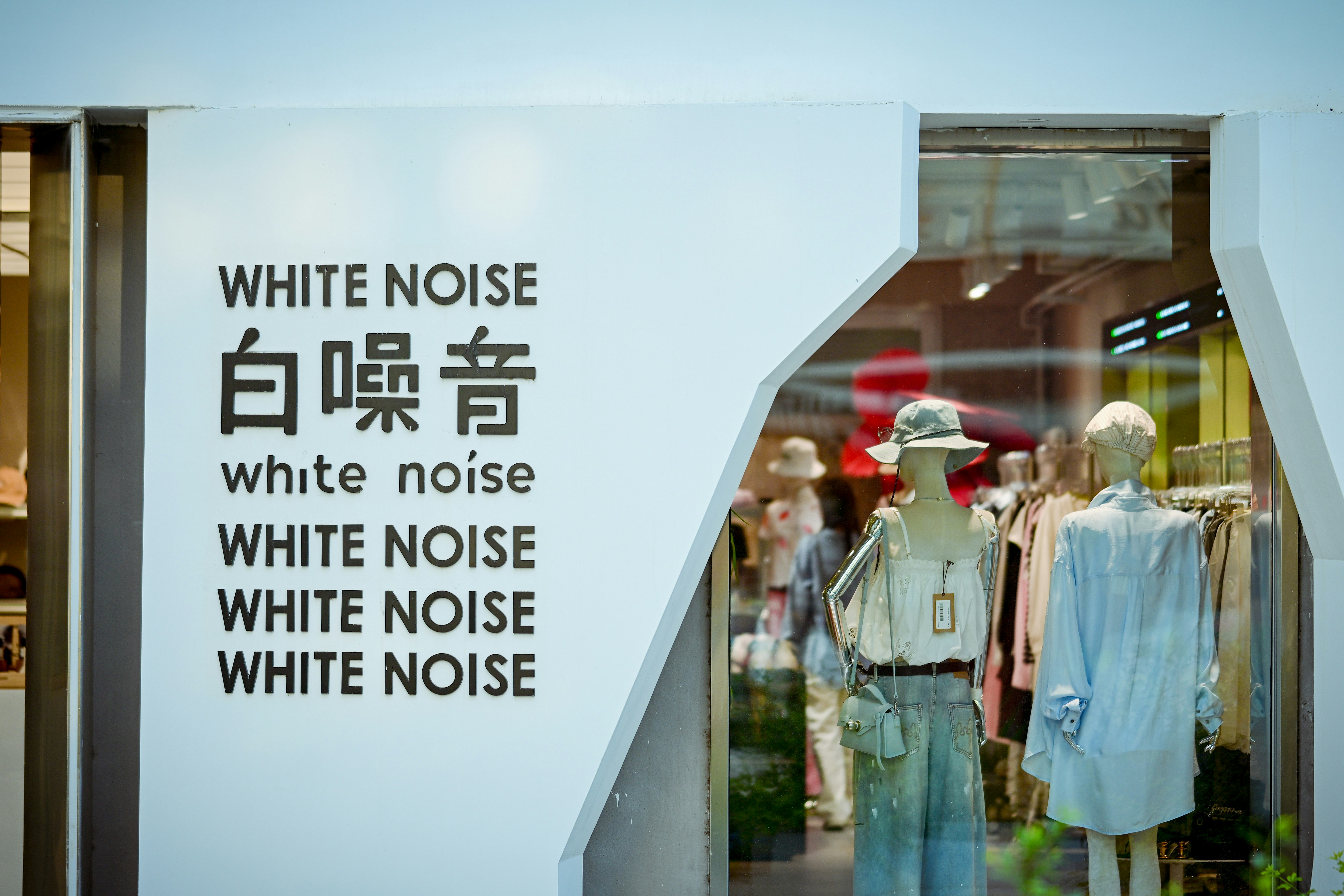 Store entrance with 'white noise' sign and mannequins displaying clothes.