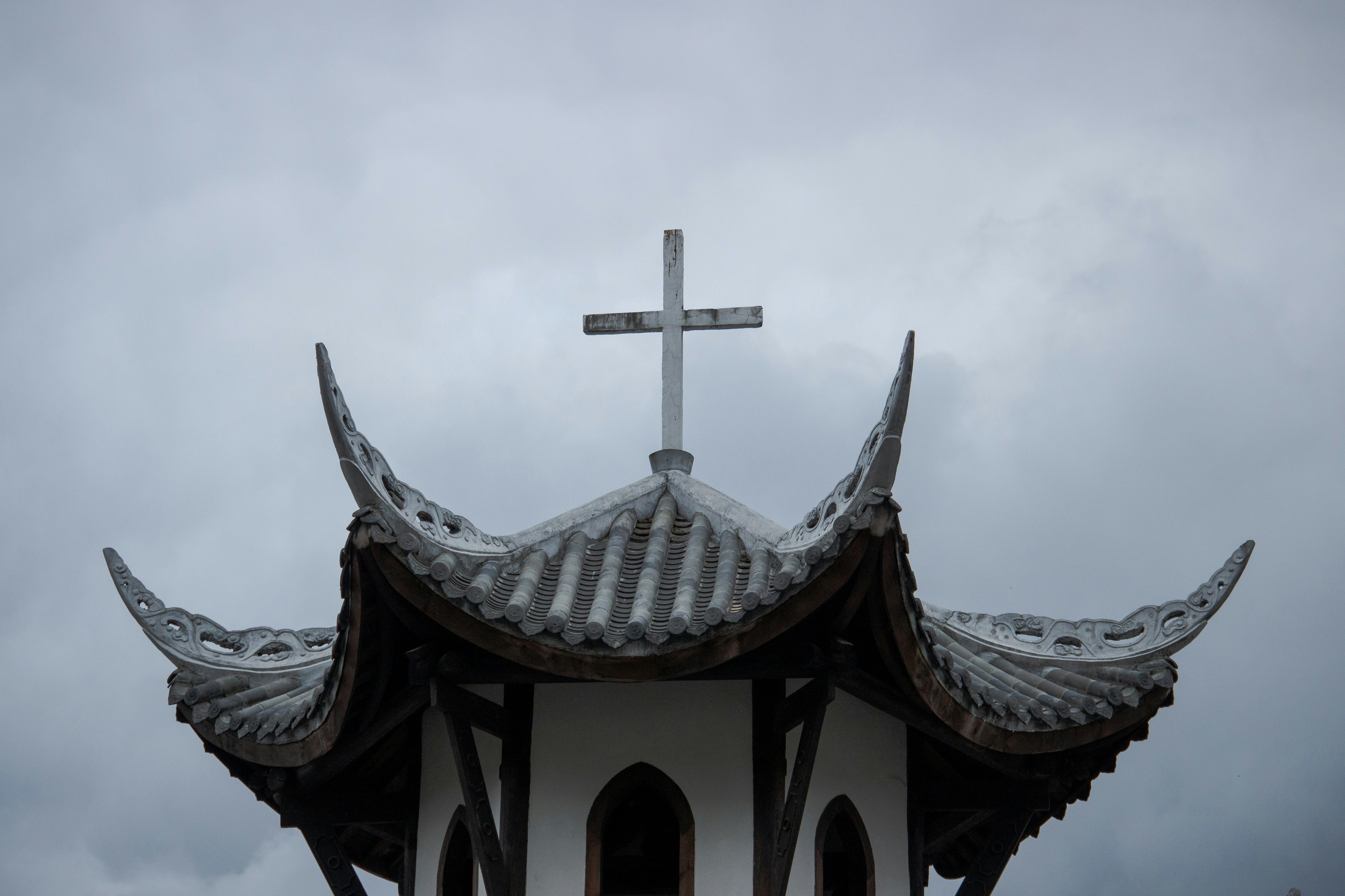 Cross atop a curved-tiled pavilion under a brooding sky