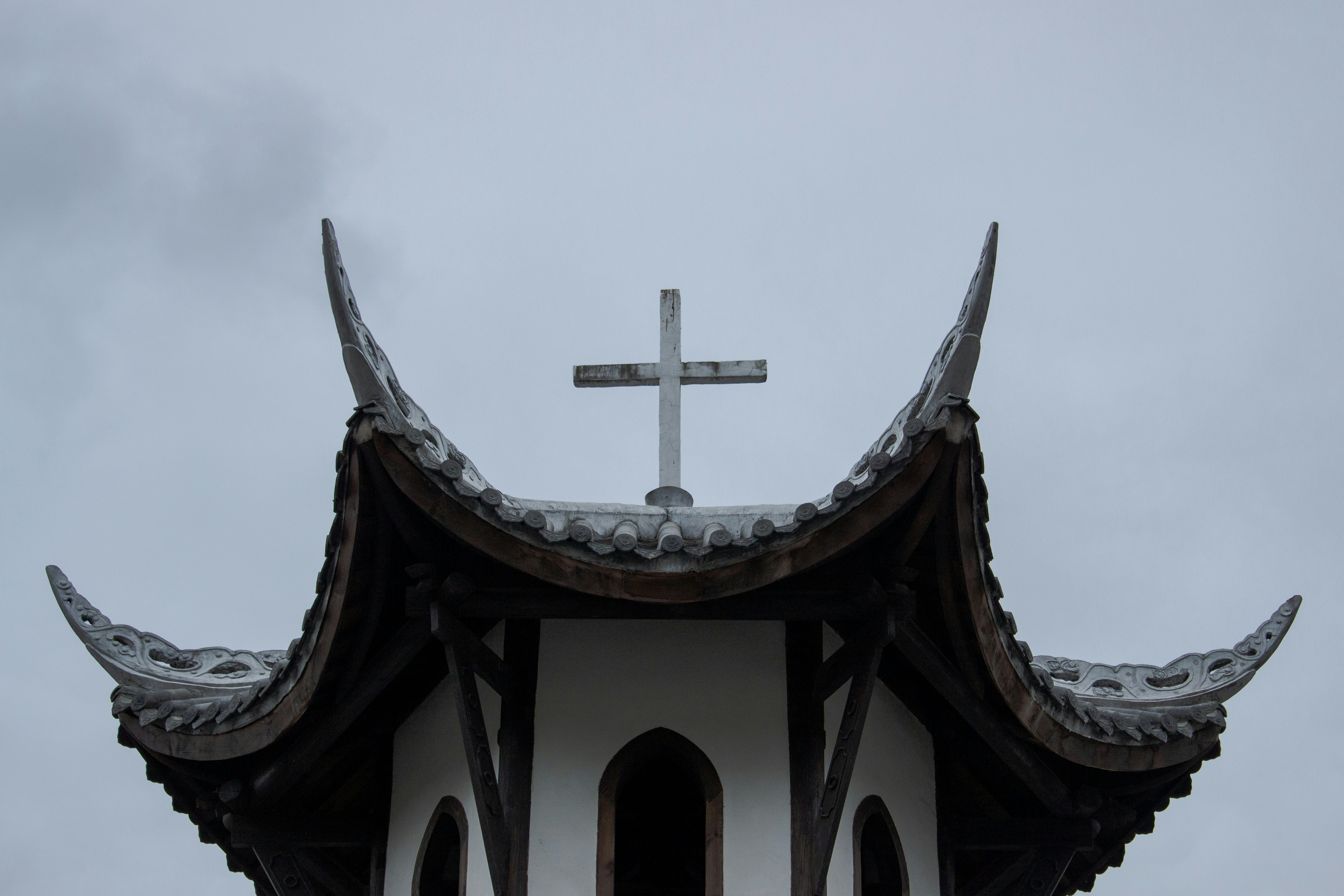 Cross atop the curved roof: a quiet chapel silhouette against a pale sky