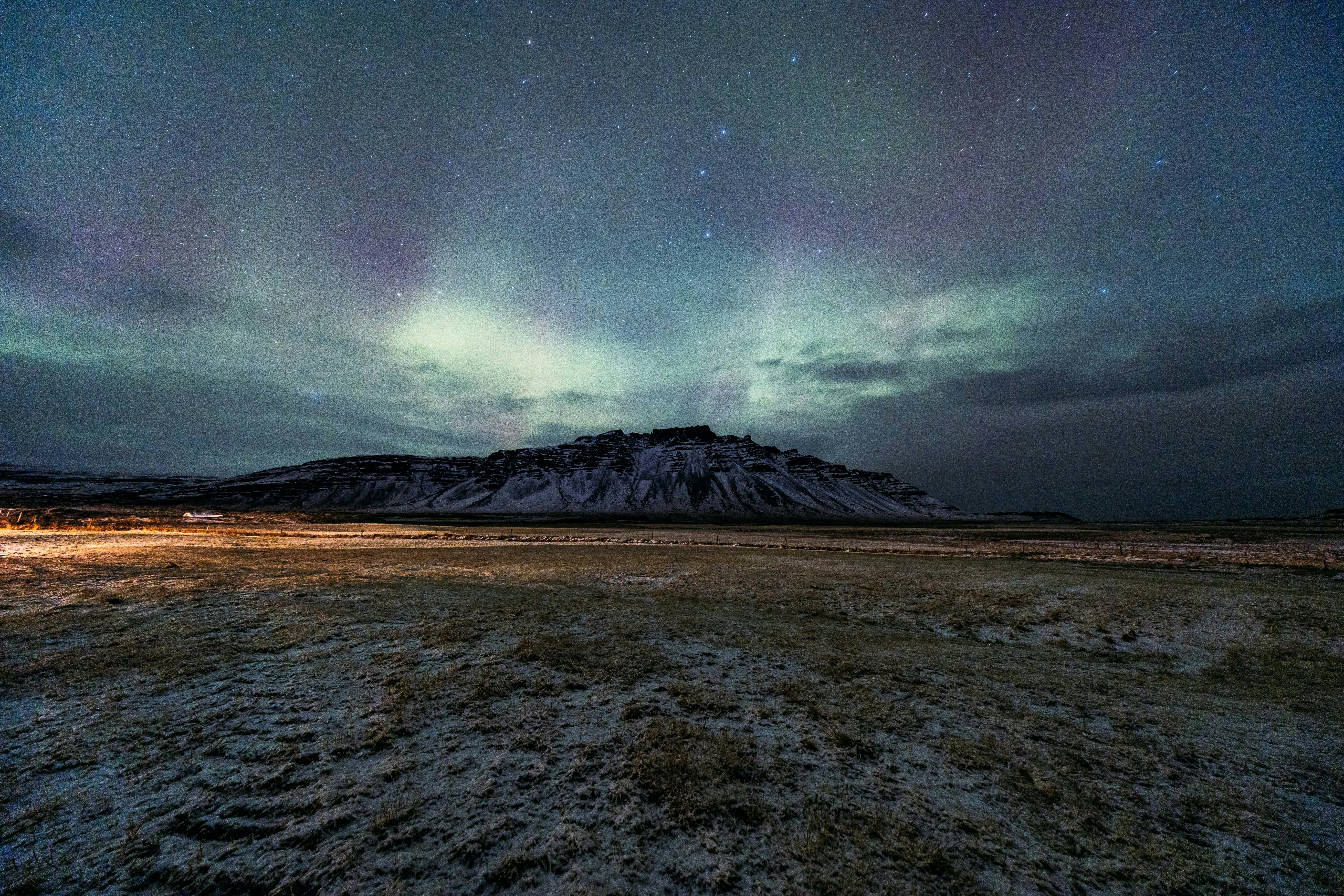 Vibrant aurora borealis illuminates a winter landscape with mountains.