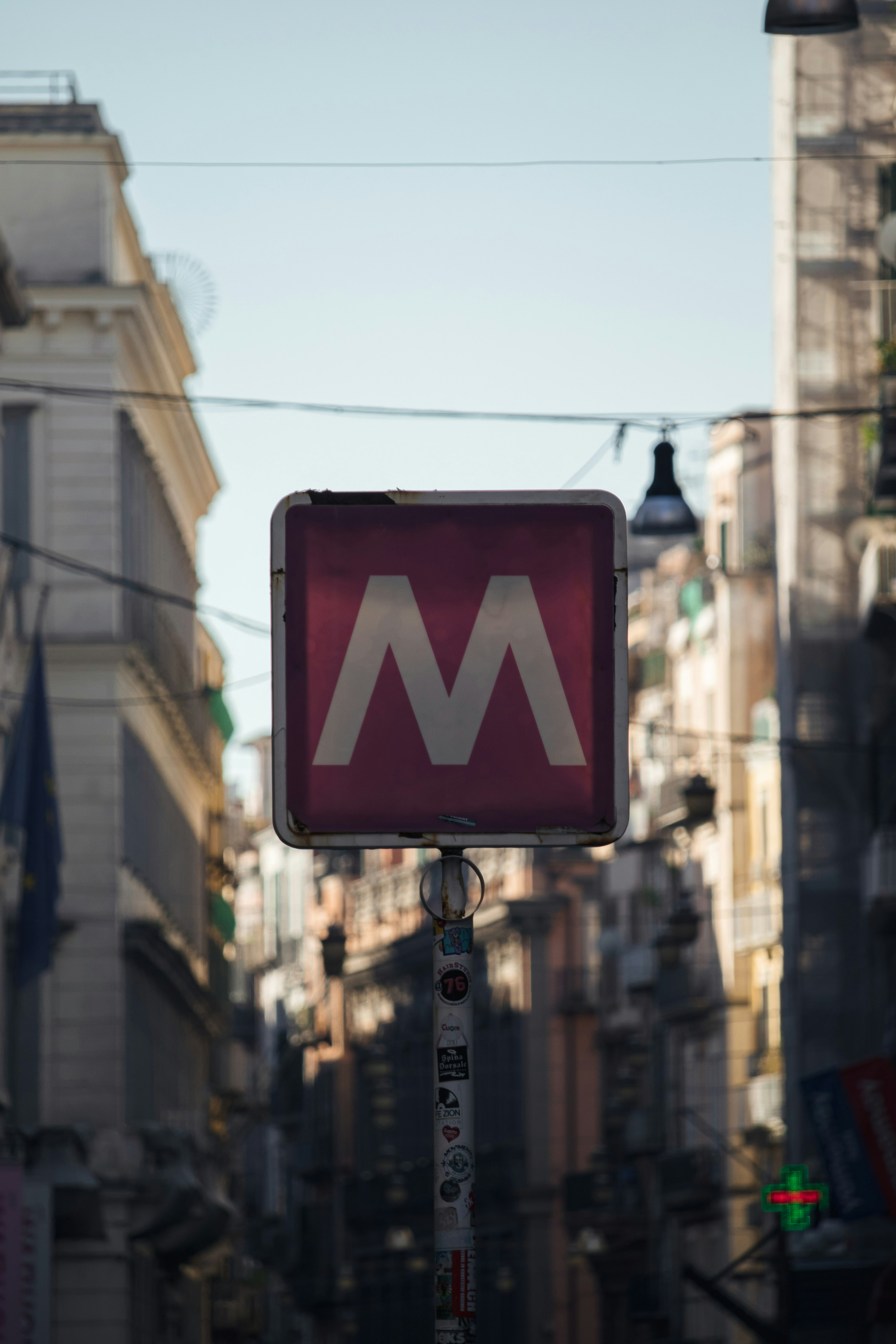 Red metro sign with a white m in a city.