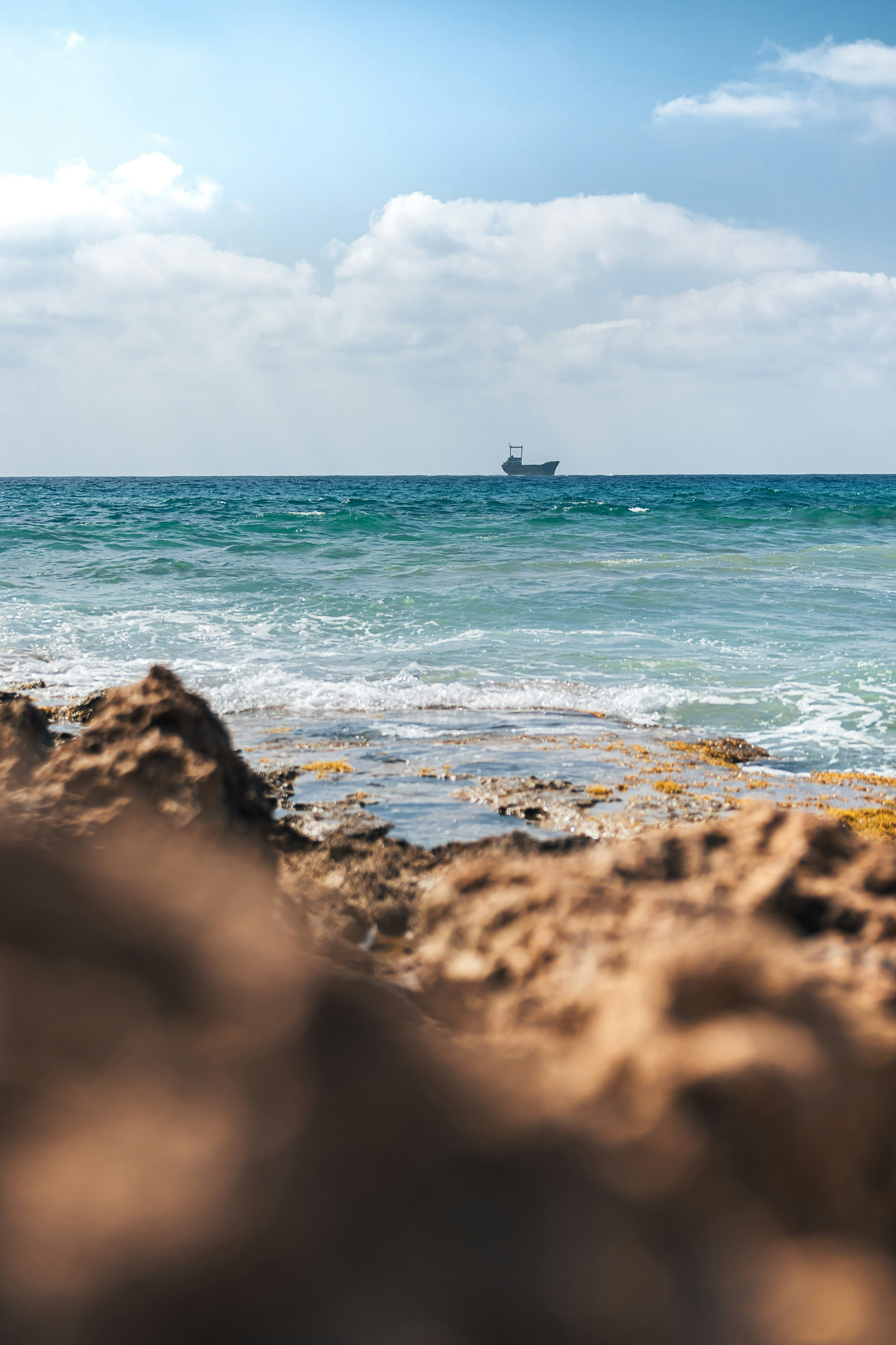 Far Horizon: A solitary ship at sea beyond a rocky shore