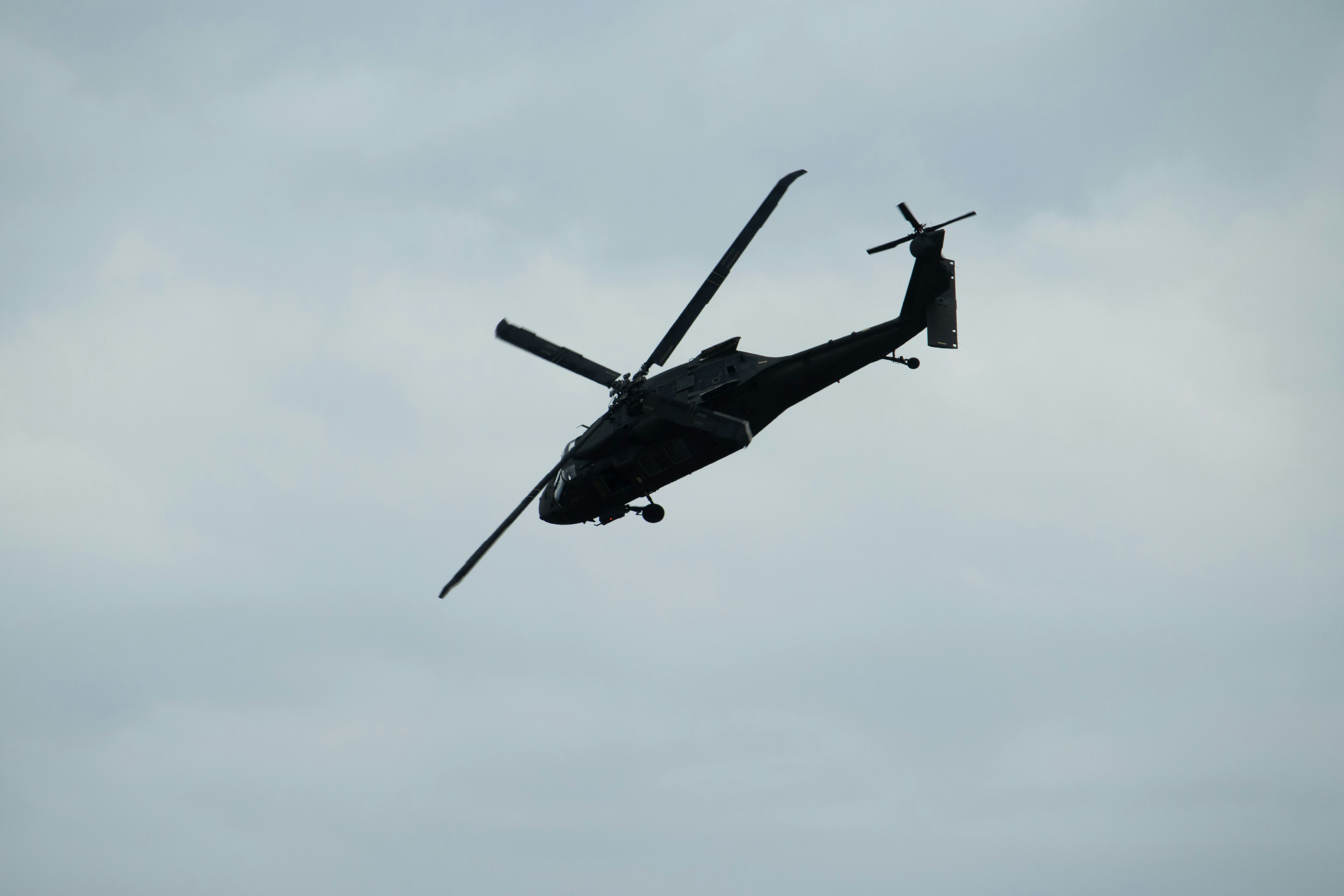 Constrained descent: helicopter carving a slow arc against a pale sky