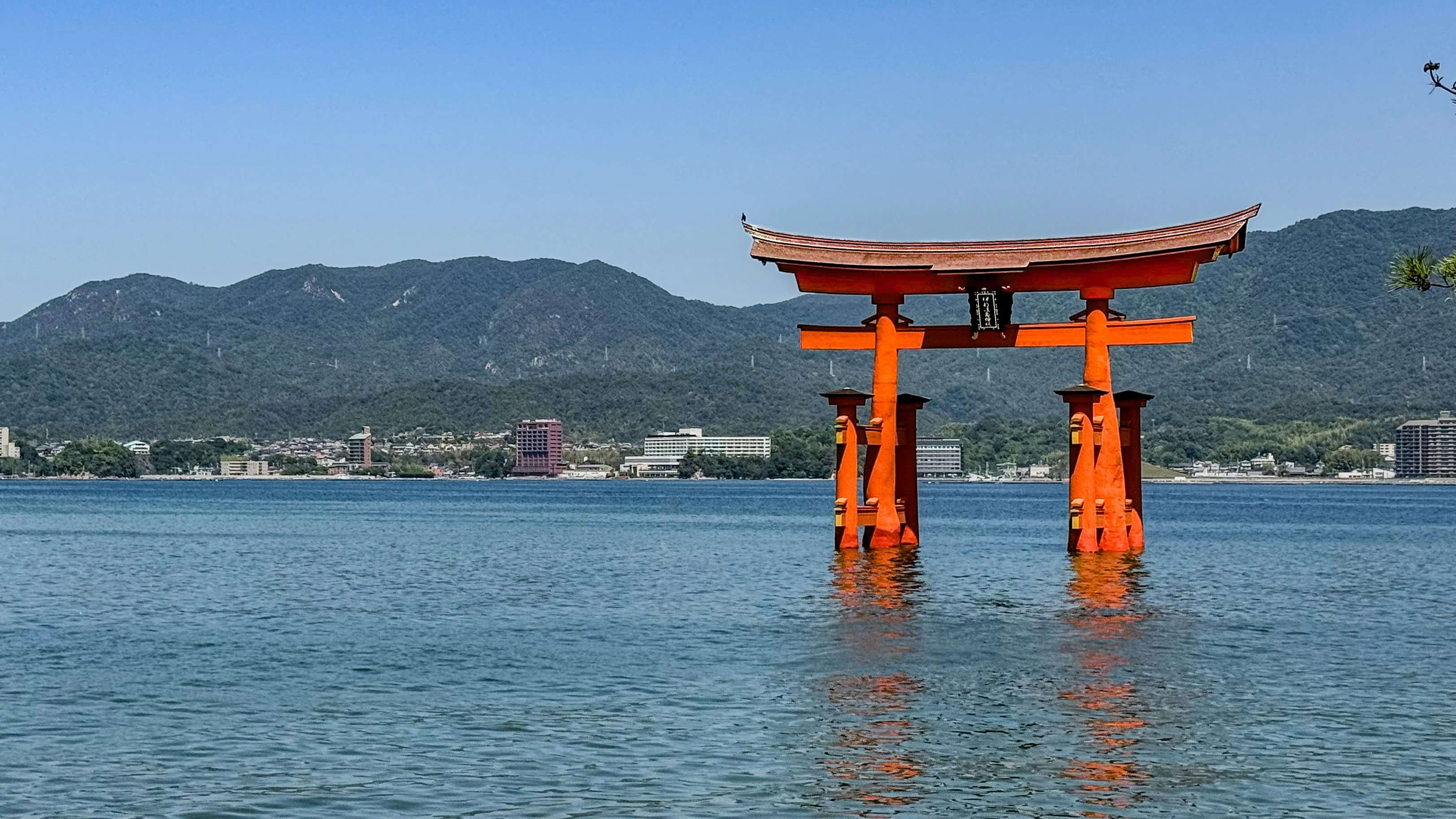 A vibrant orange torii gate stands in calm blue water.