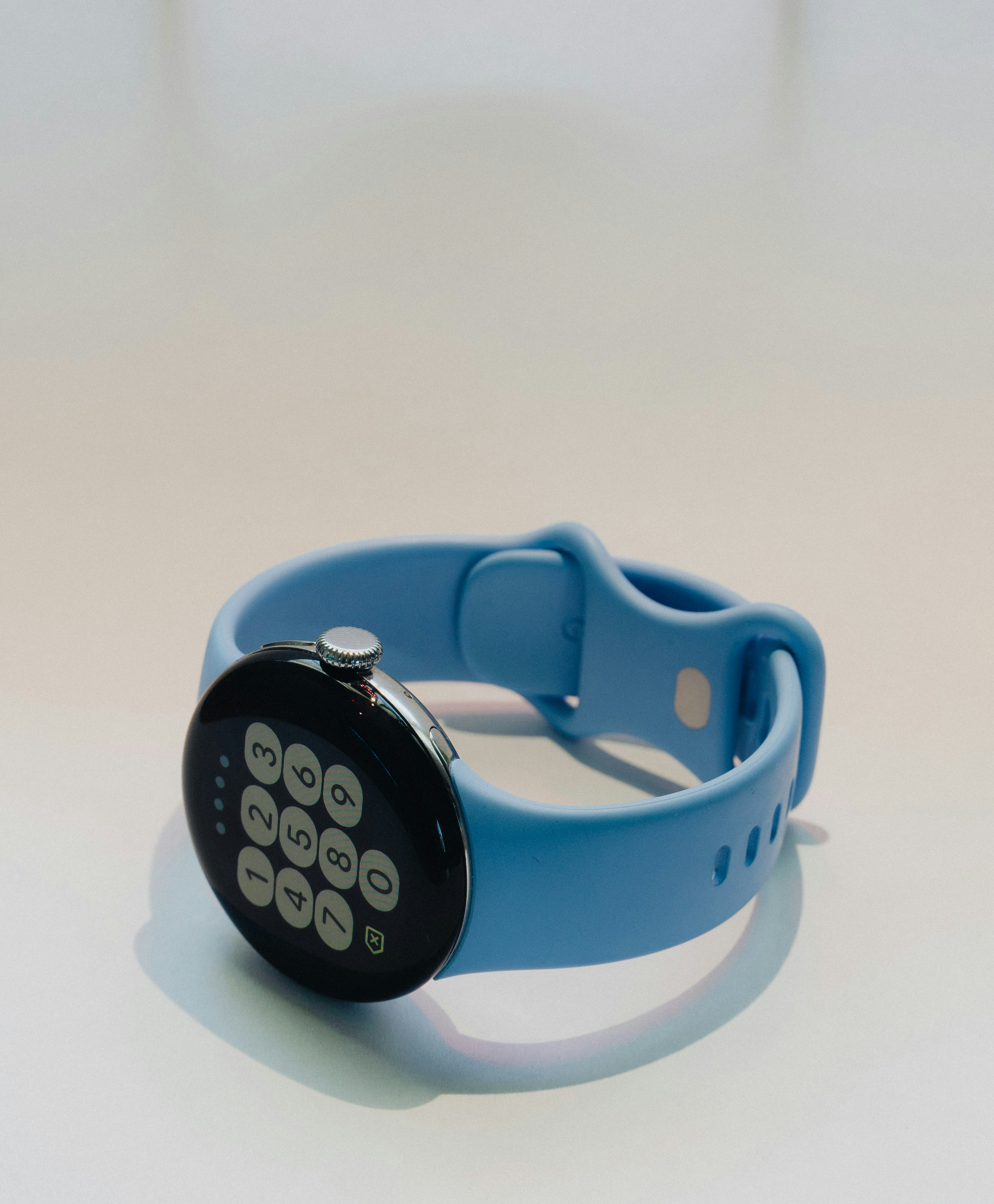 A light blue smartwatch displaying a keypad on its screen.