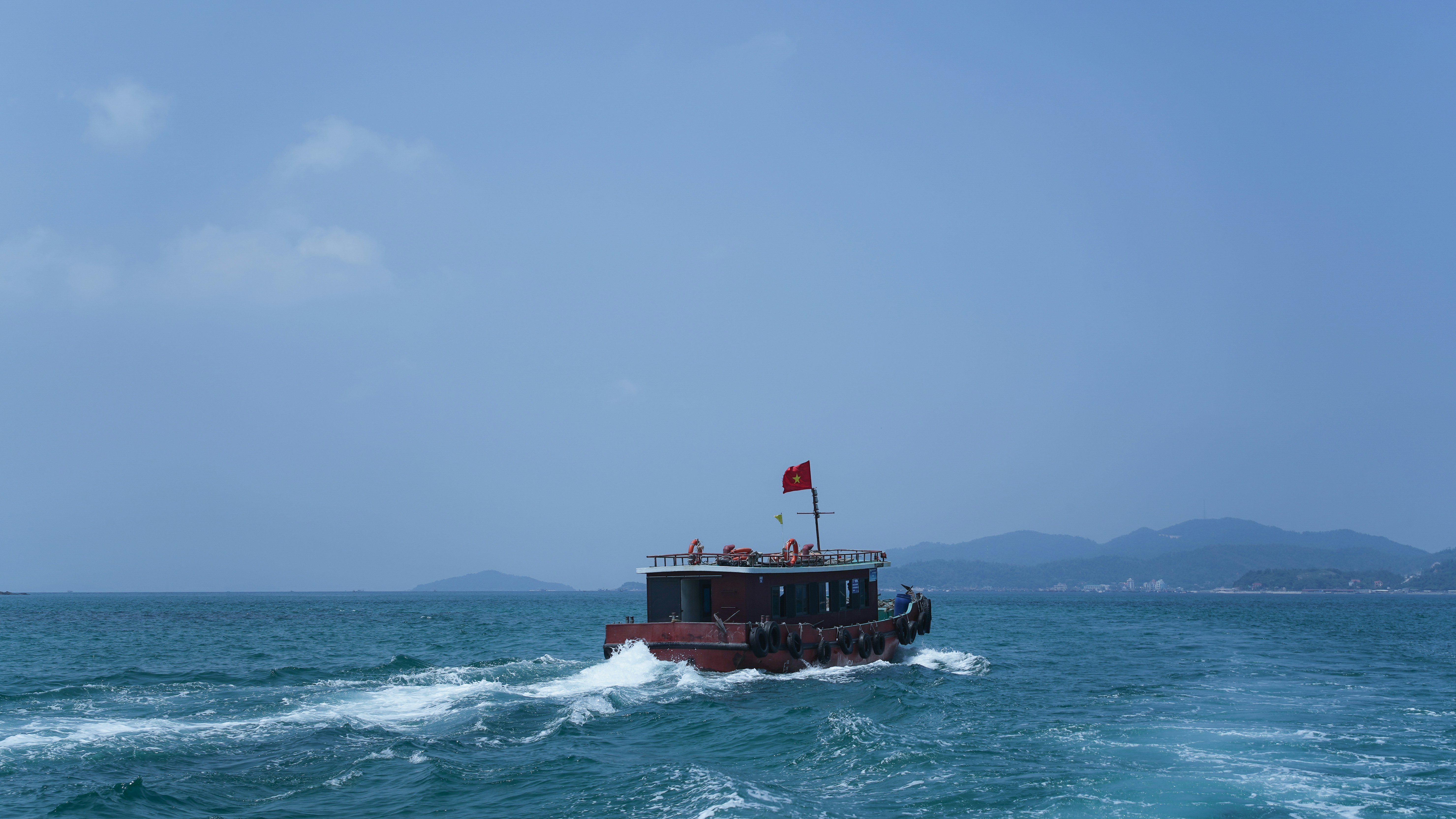 Red-topped ferry carving through blue seas toward distant shores