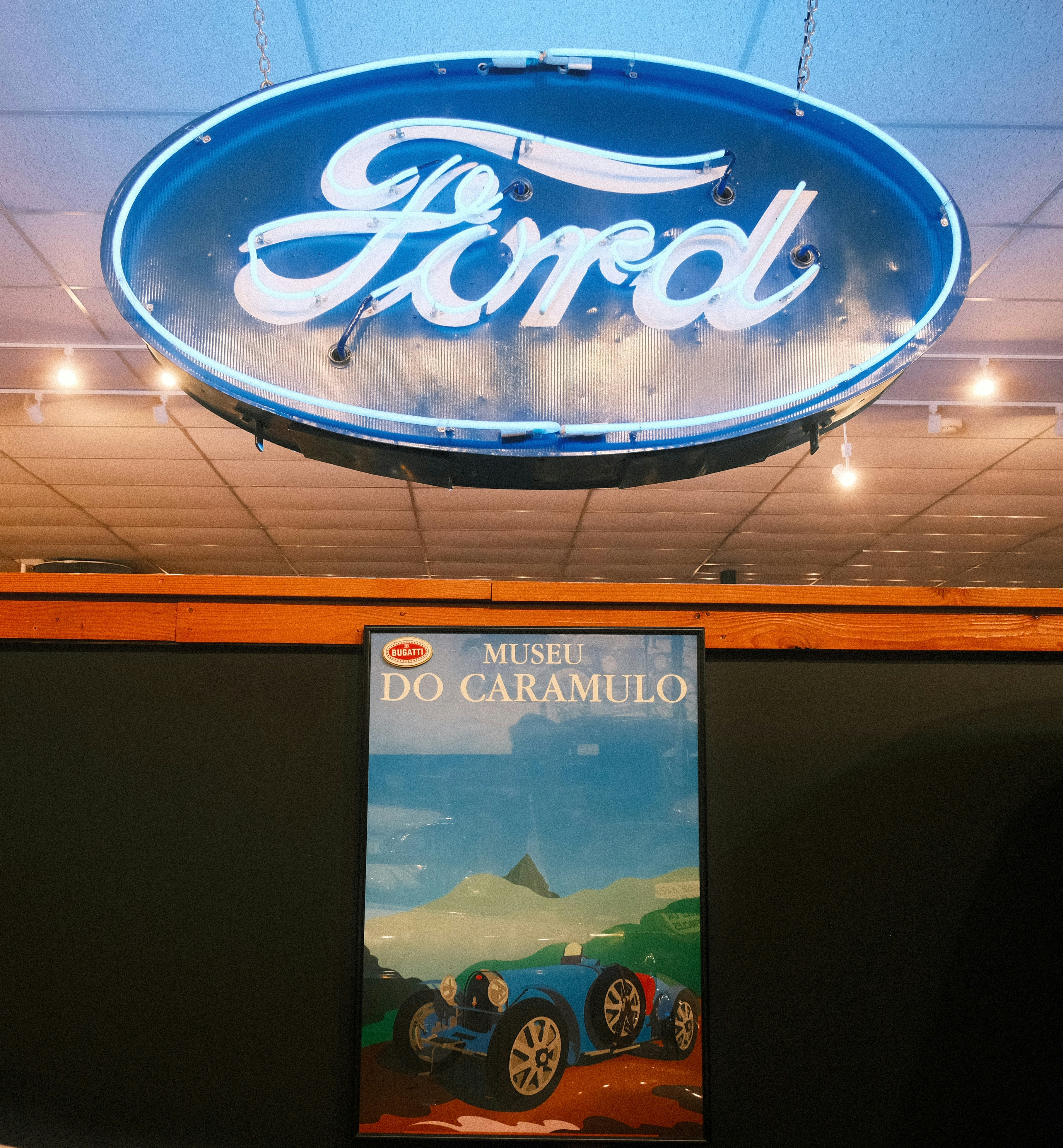 A neon ford sign hangs above a classic car poster.