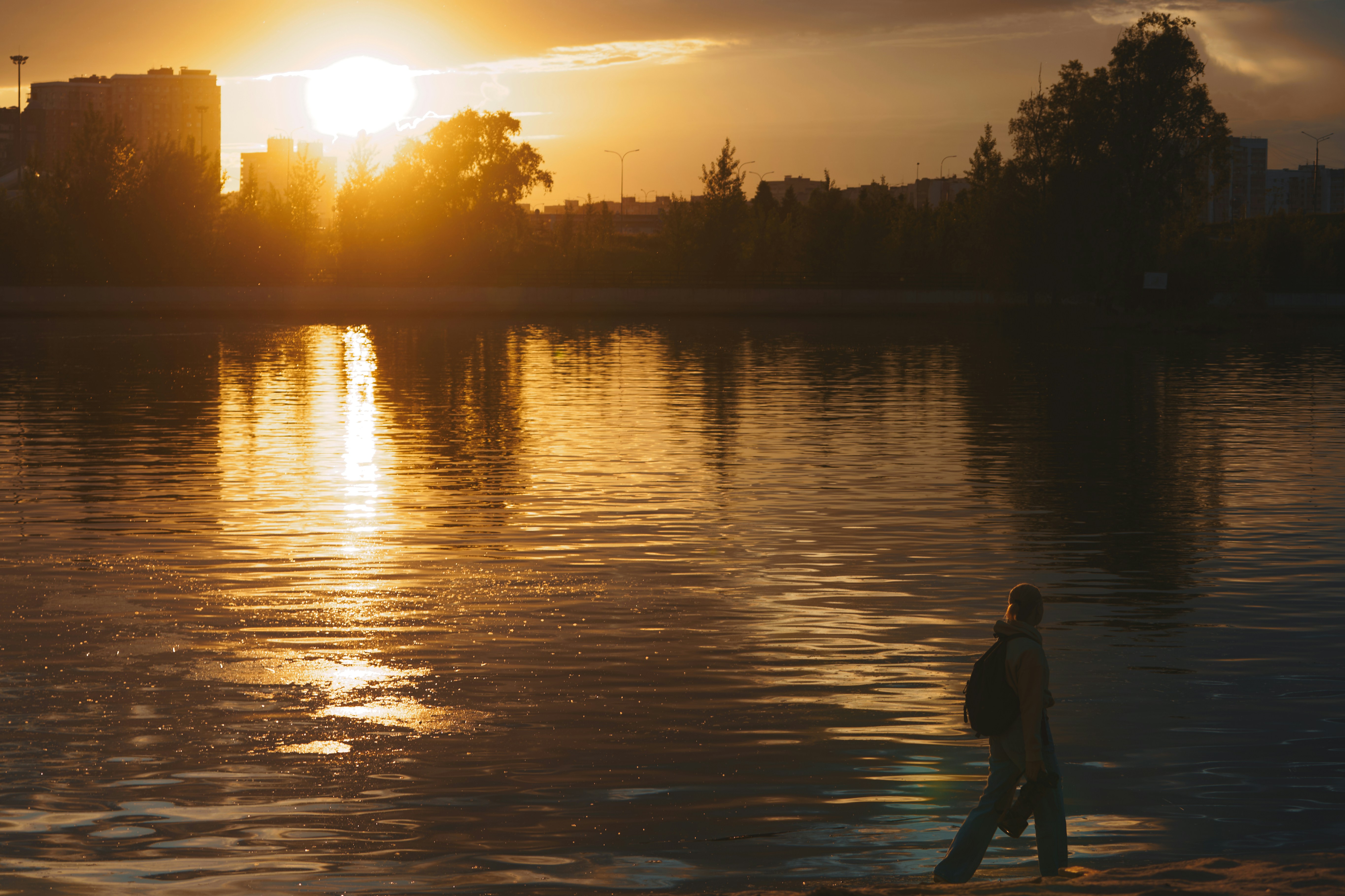 Sunlit Reflection: A lone figure walks the river at dusk