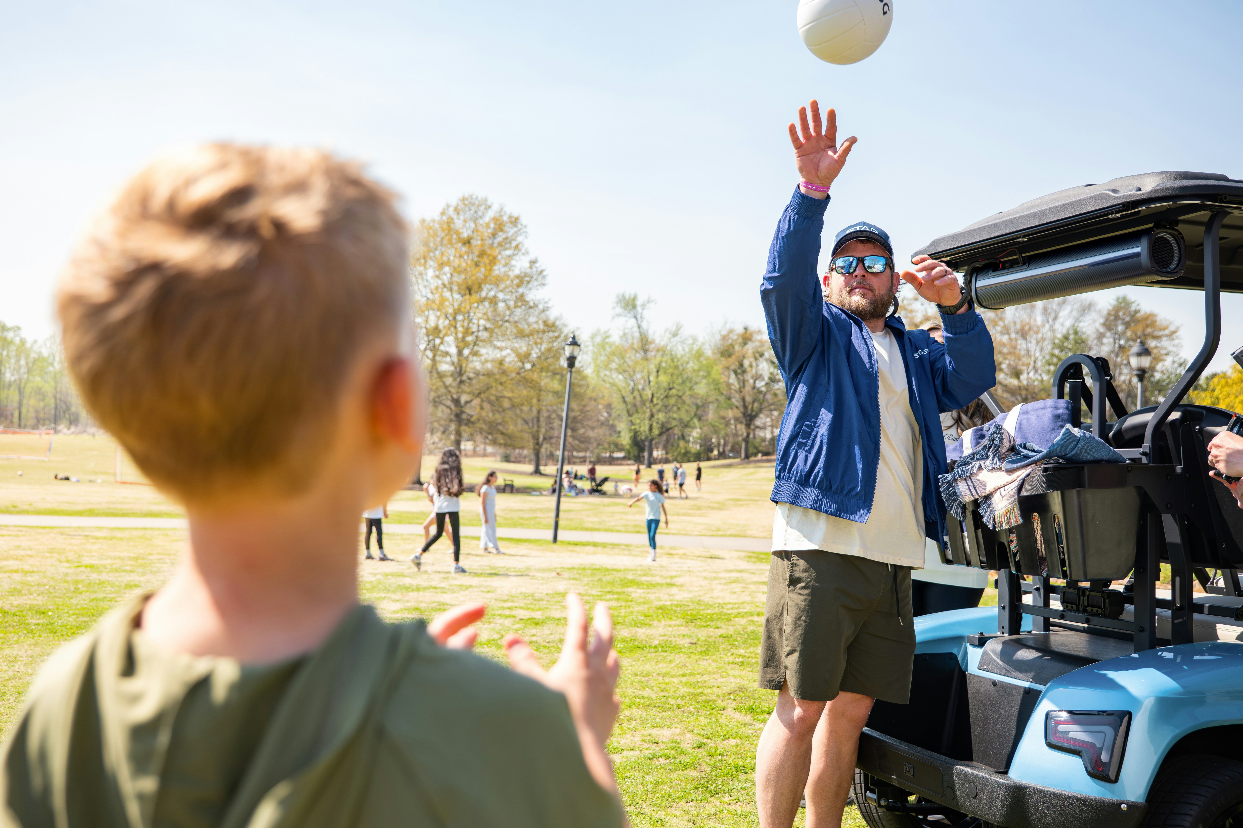 A man and boy playing volleyball near a golf cart.