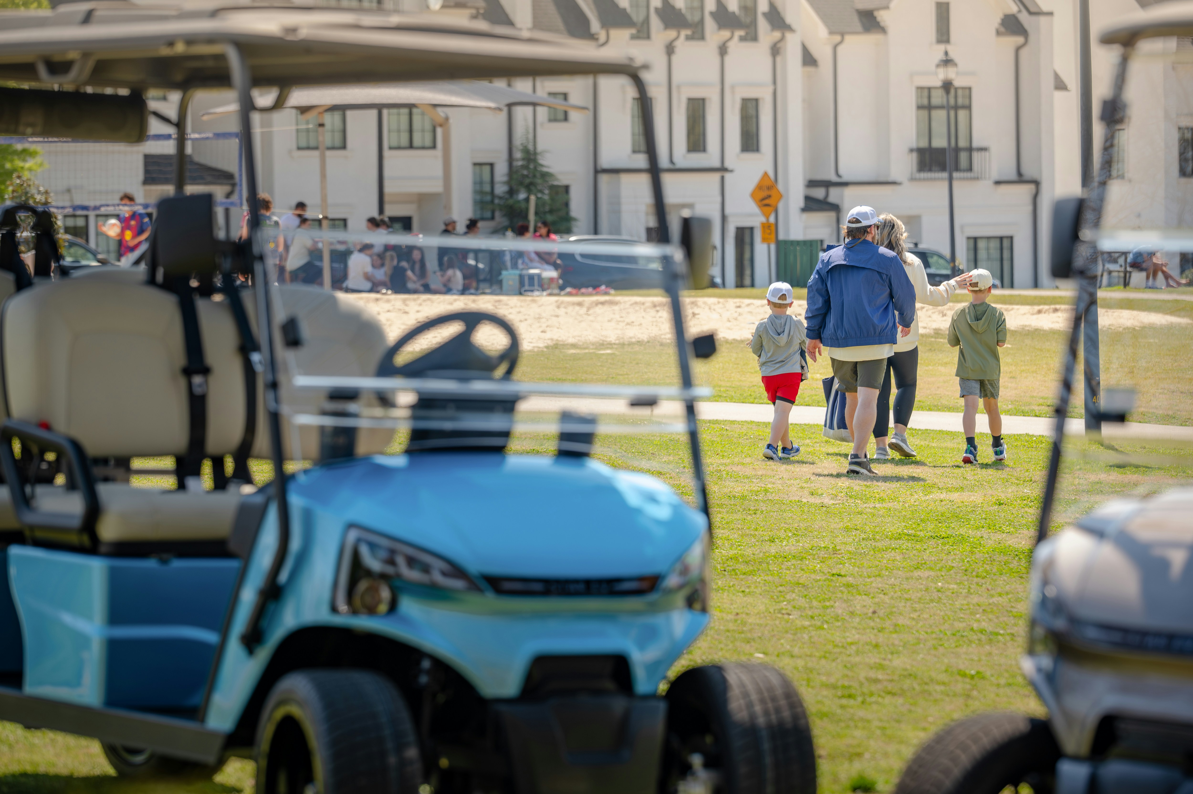 Children and a caregiver in a sunlit park framed by blue golf carts
