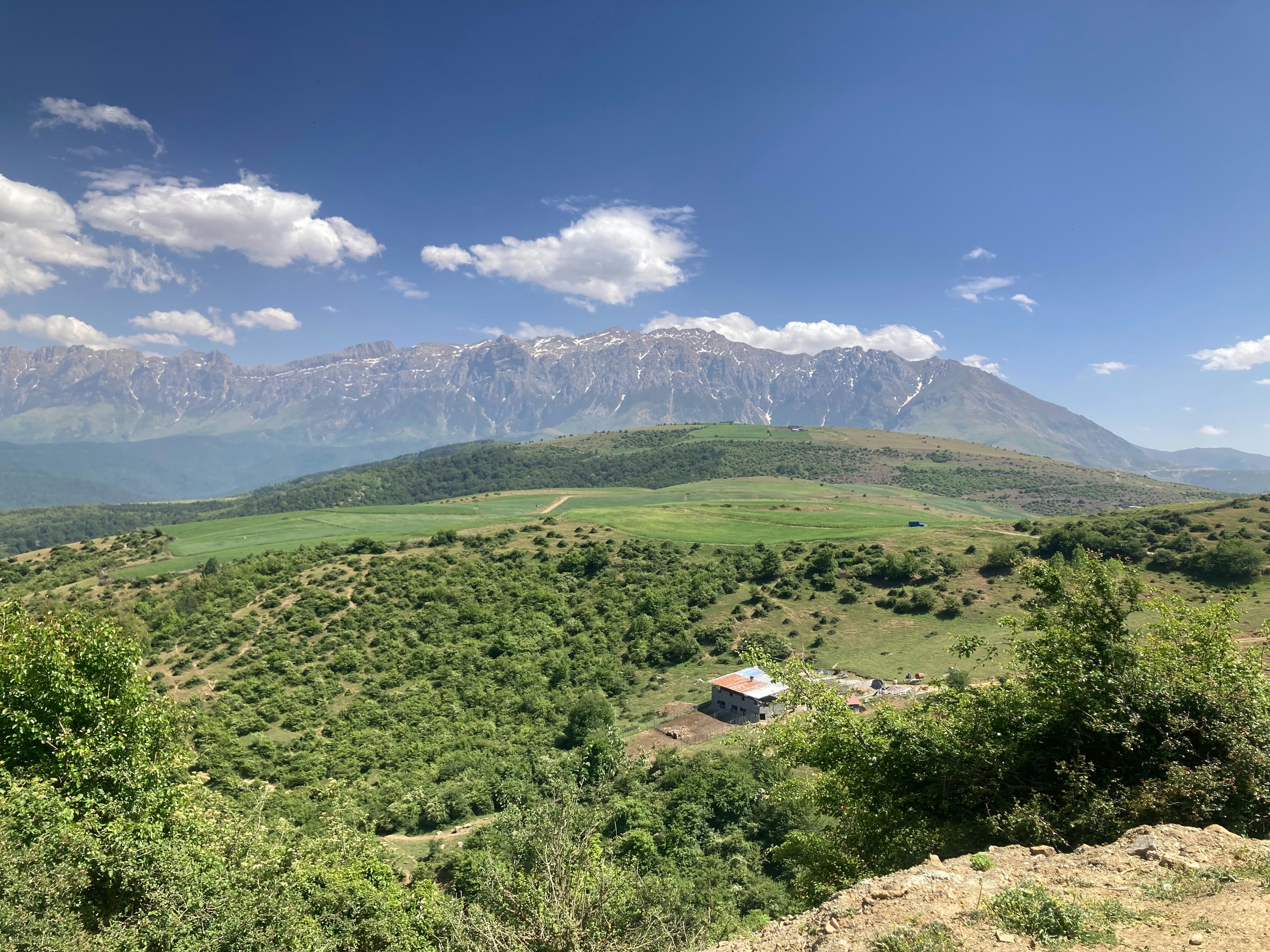 Vast green landscape with distant mountains and a small building.