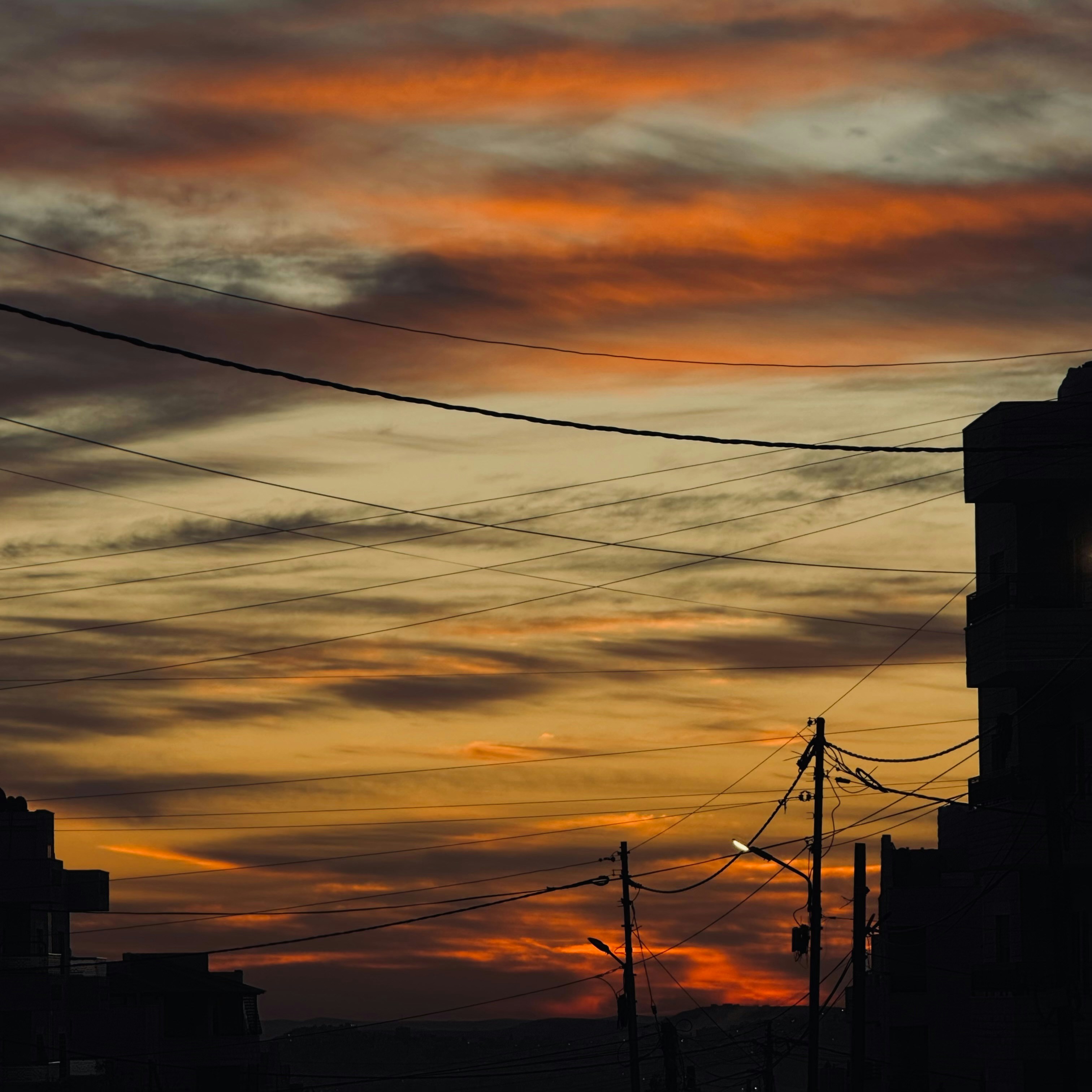 Colorful sunset over silhouetted buildings and power lines.