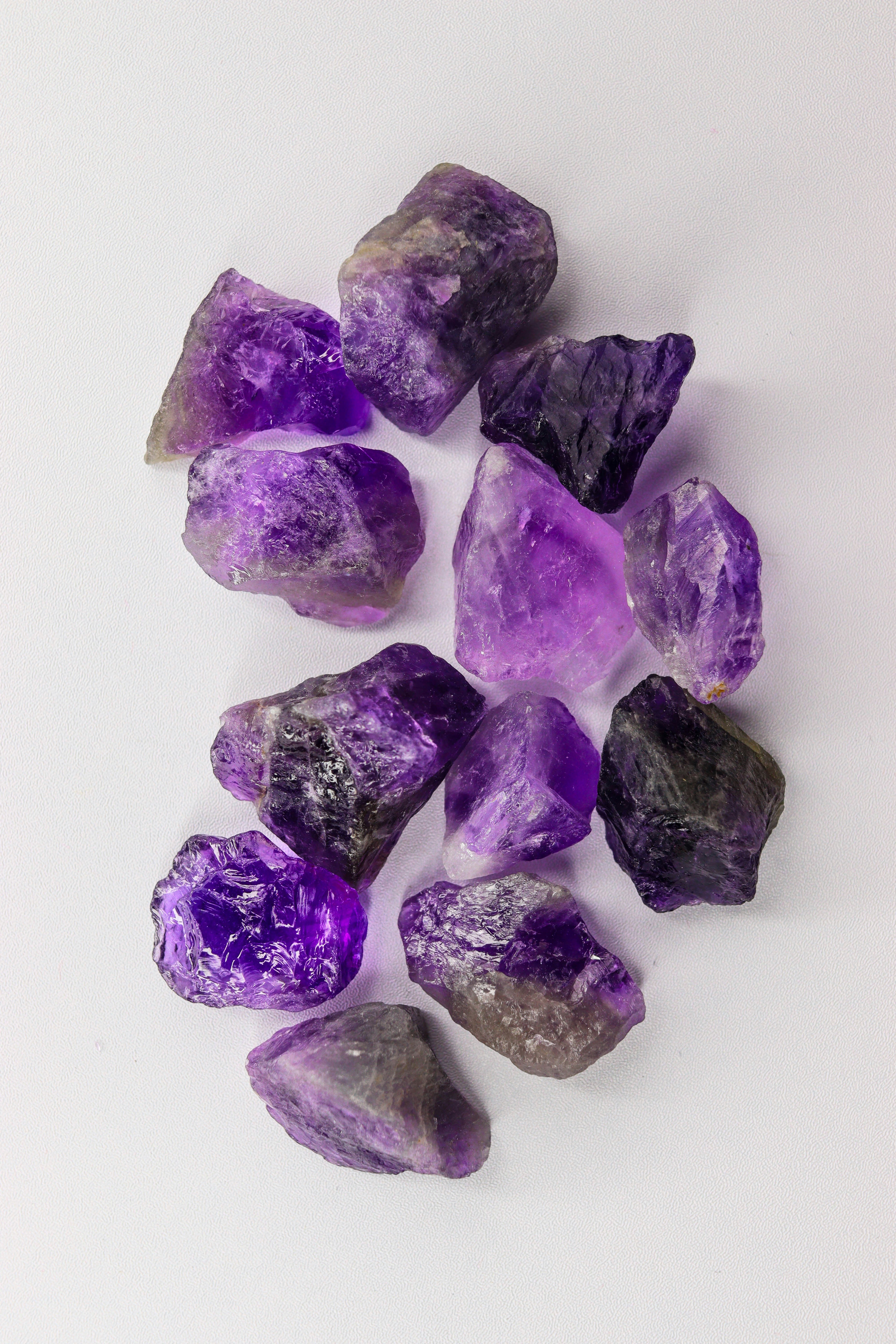 Grouping of rough amethyst rocks arranged on a light surface, showcasing various purple tones and textures; a still-life study of mineral translucence.