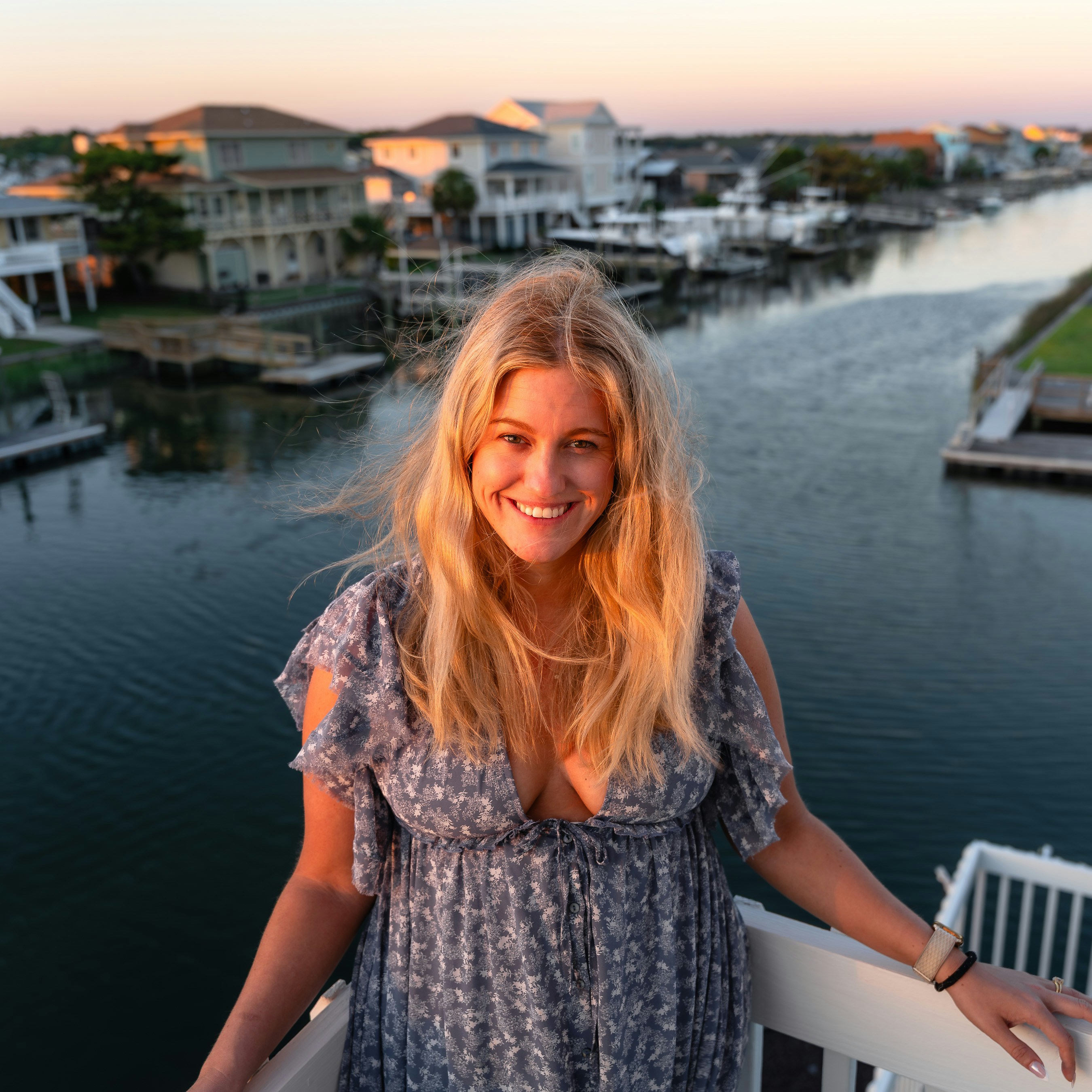 Woman smiling on a balcony over a canal at sunset.