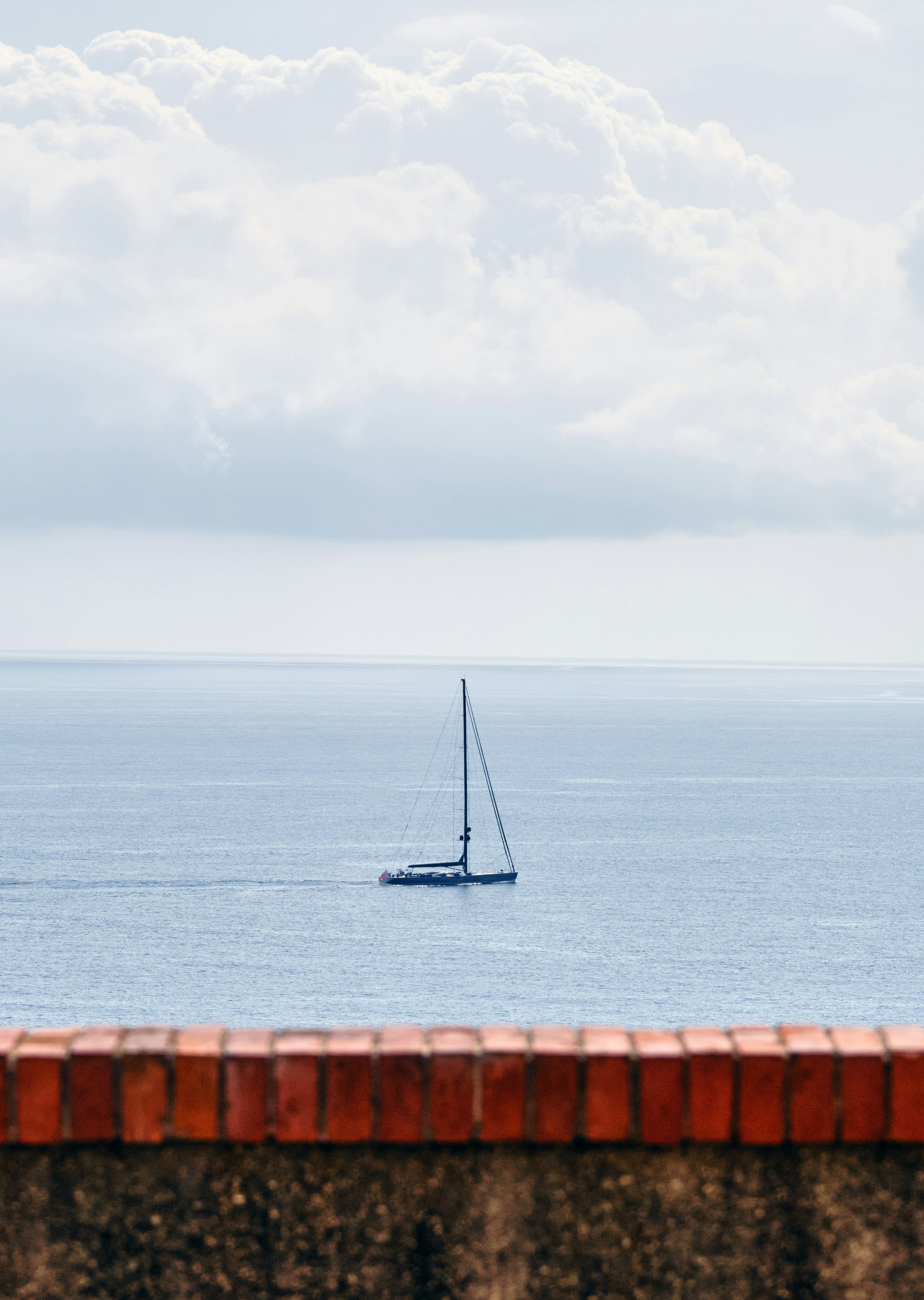 Sailboat at the Horizon: A Quiet Seascape Above a Brick-Foreground