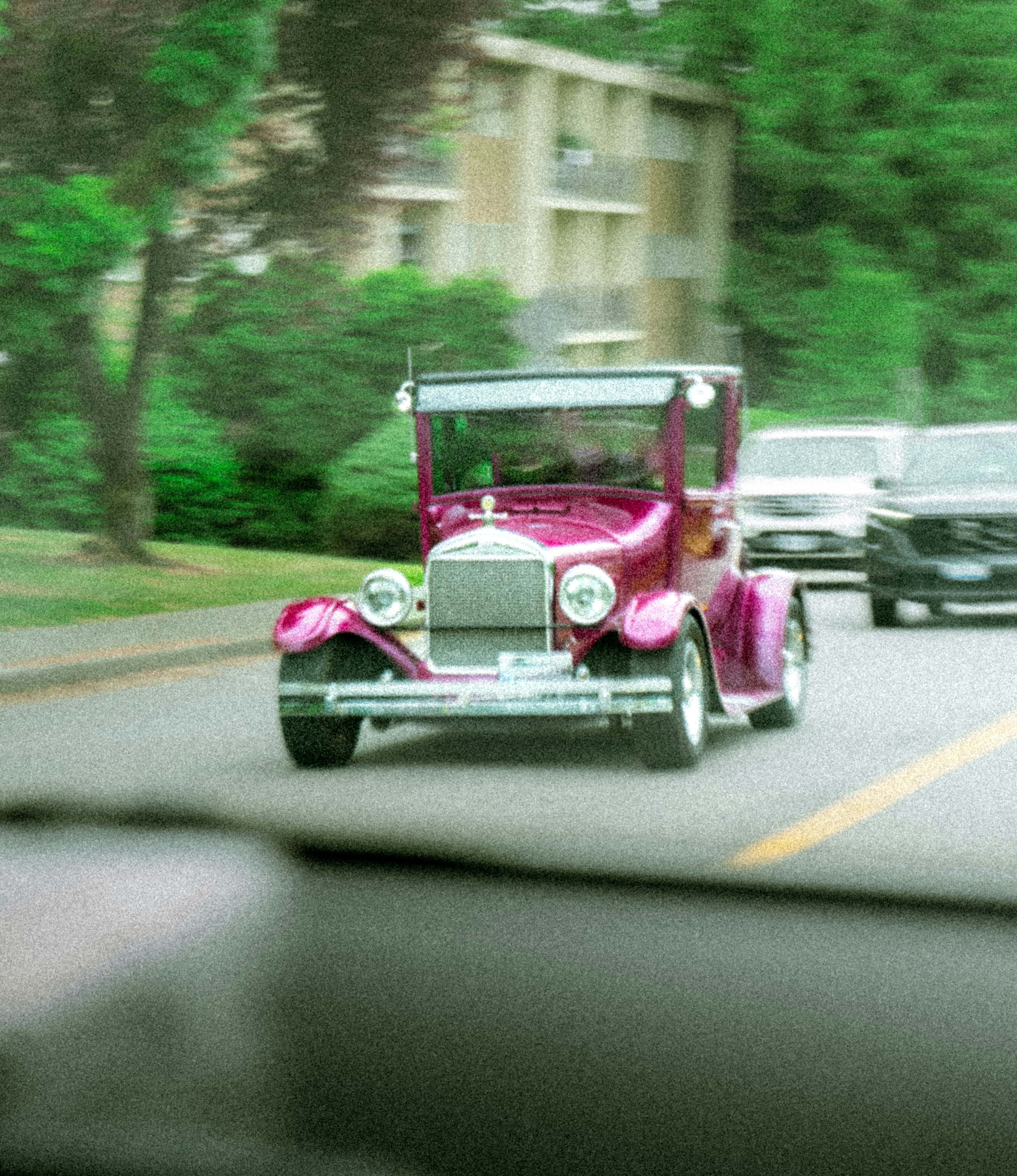 Vintage magenta automobile tears through a tree-lined street