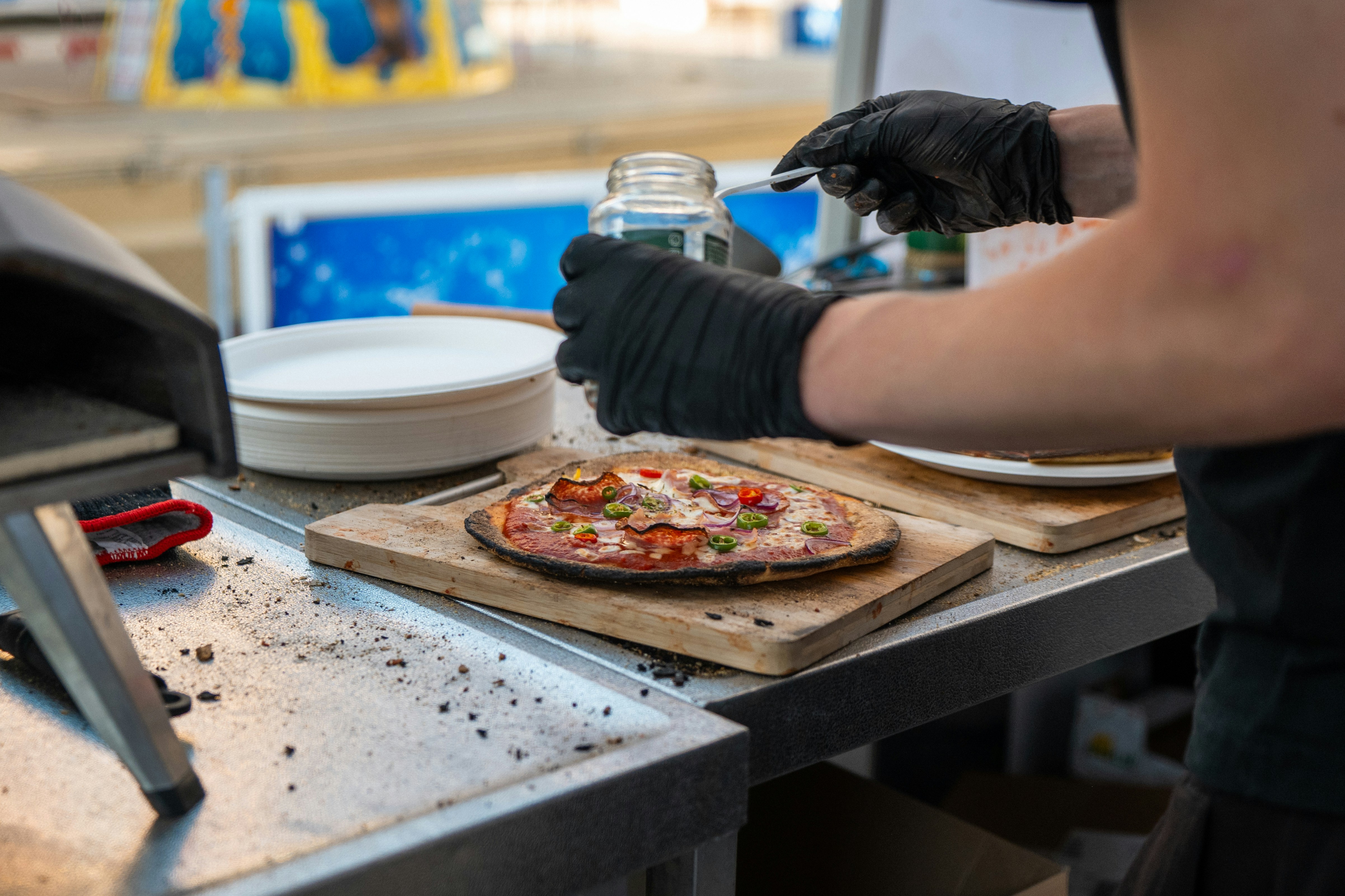 Chef in black gloves preparing pizza on a wooden board.