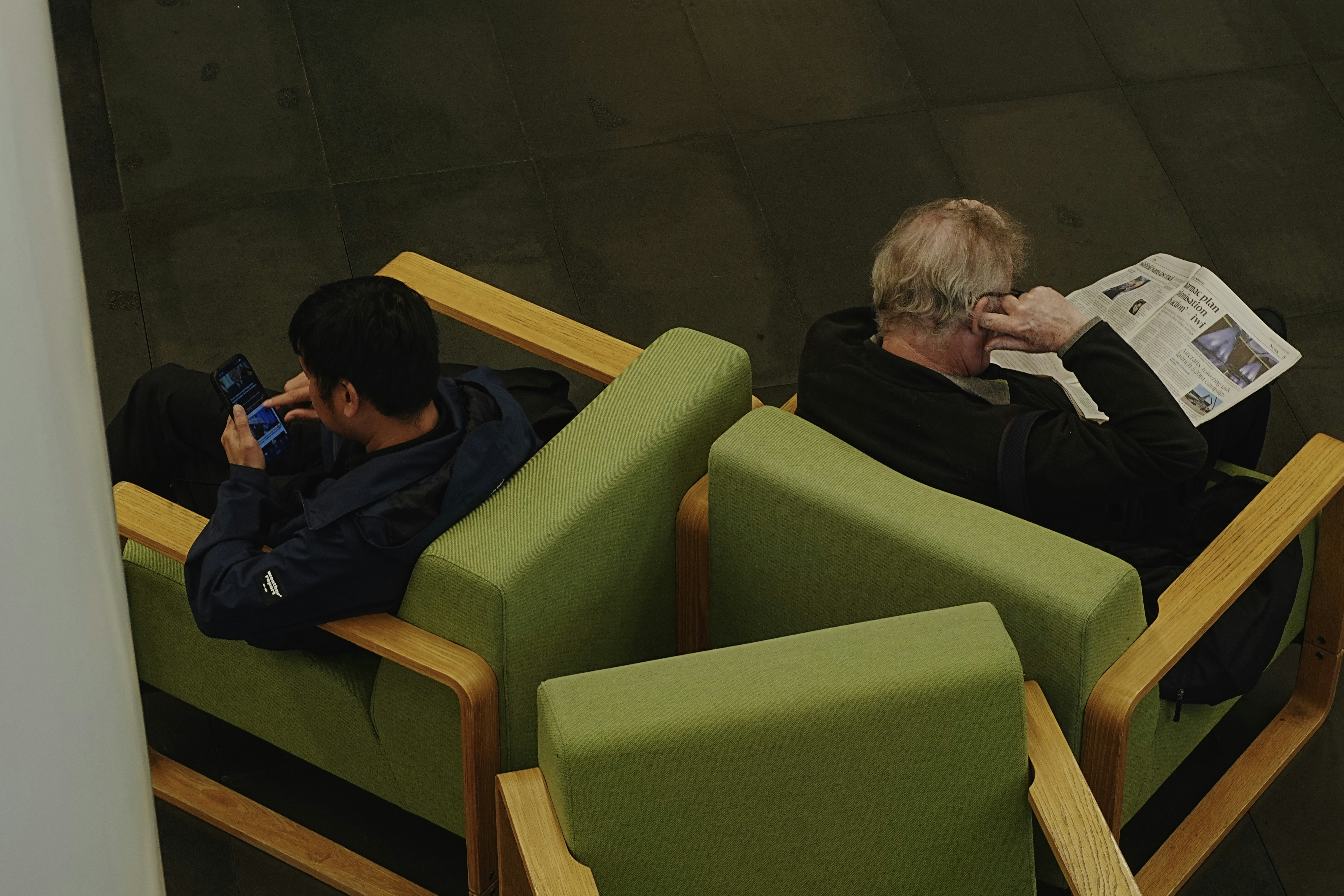 People relaxing in green chairs, reading and using a device.