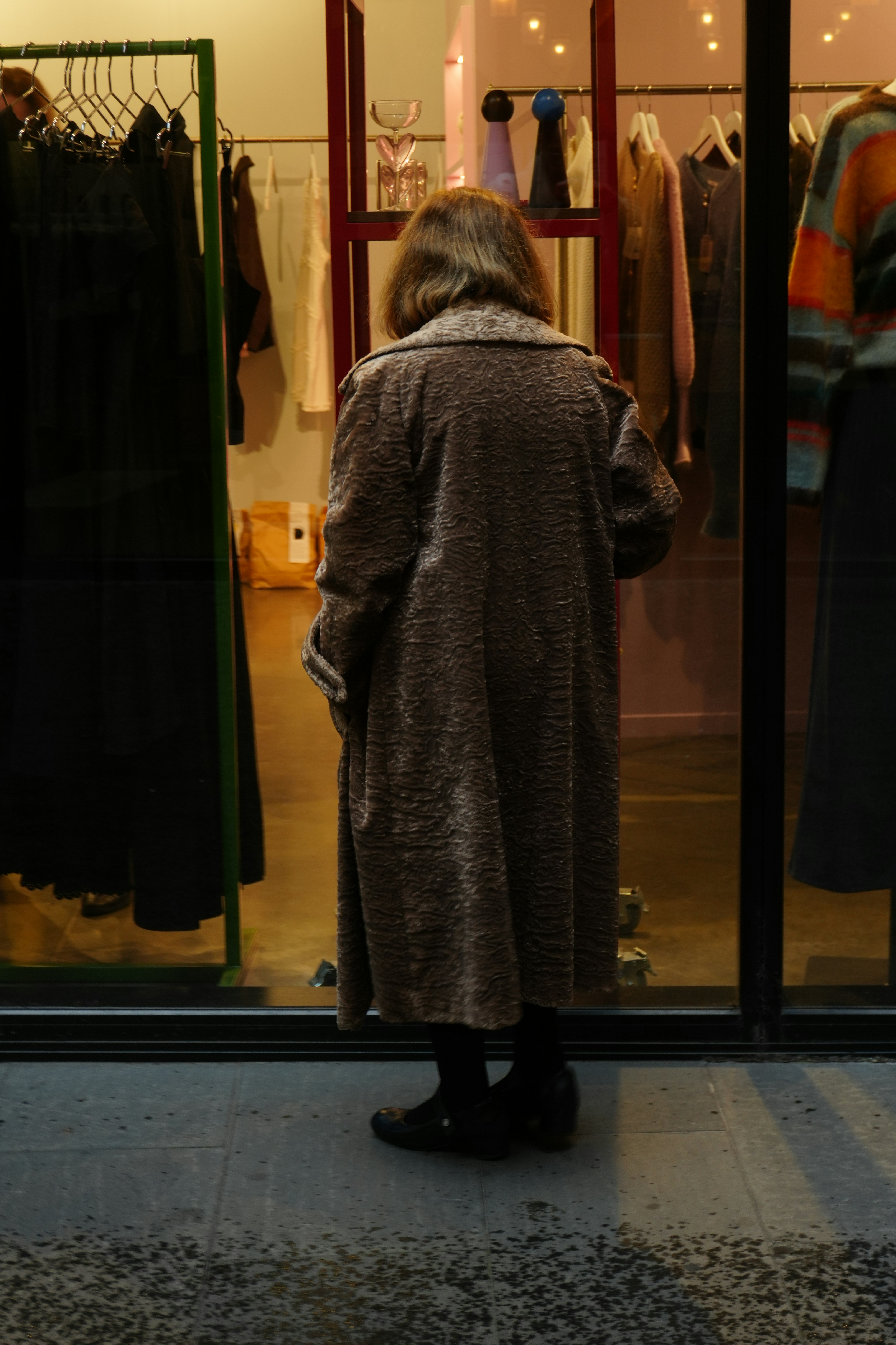 Silhouette in Velvet: A Woman in a Coat Stares Through a Boutique Window