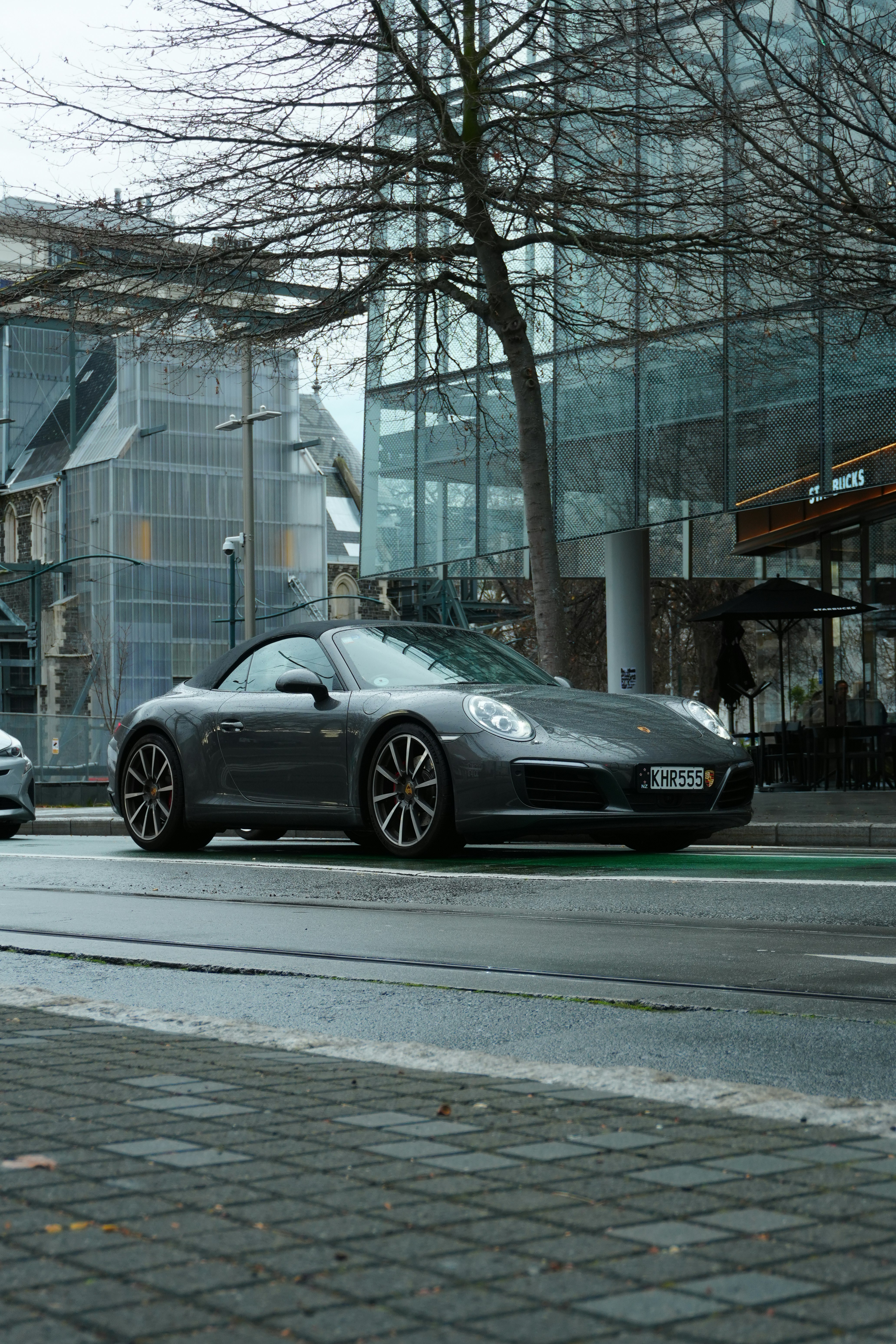 Grey porsche convertible parked on a wet city street.