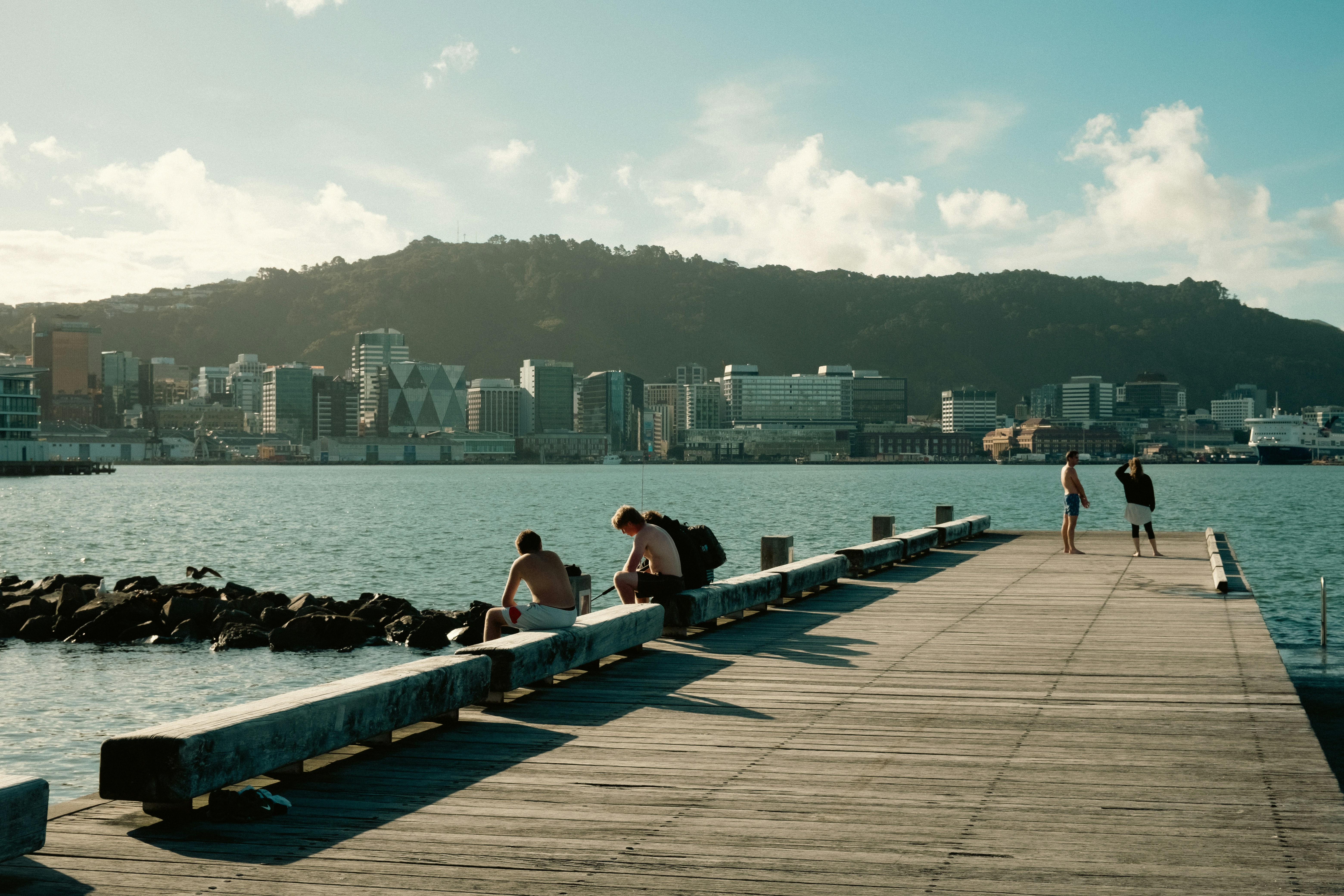 Sunlit Pier: People at the Waterfront with City Horizon