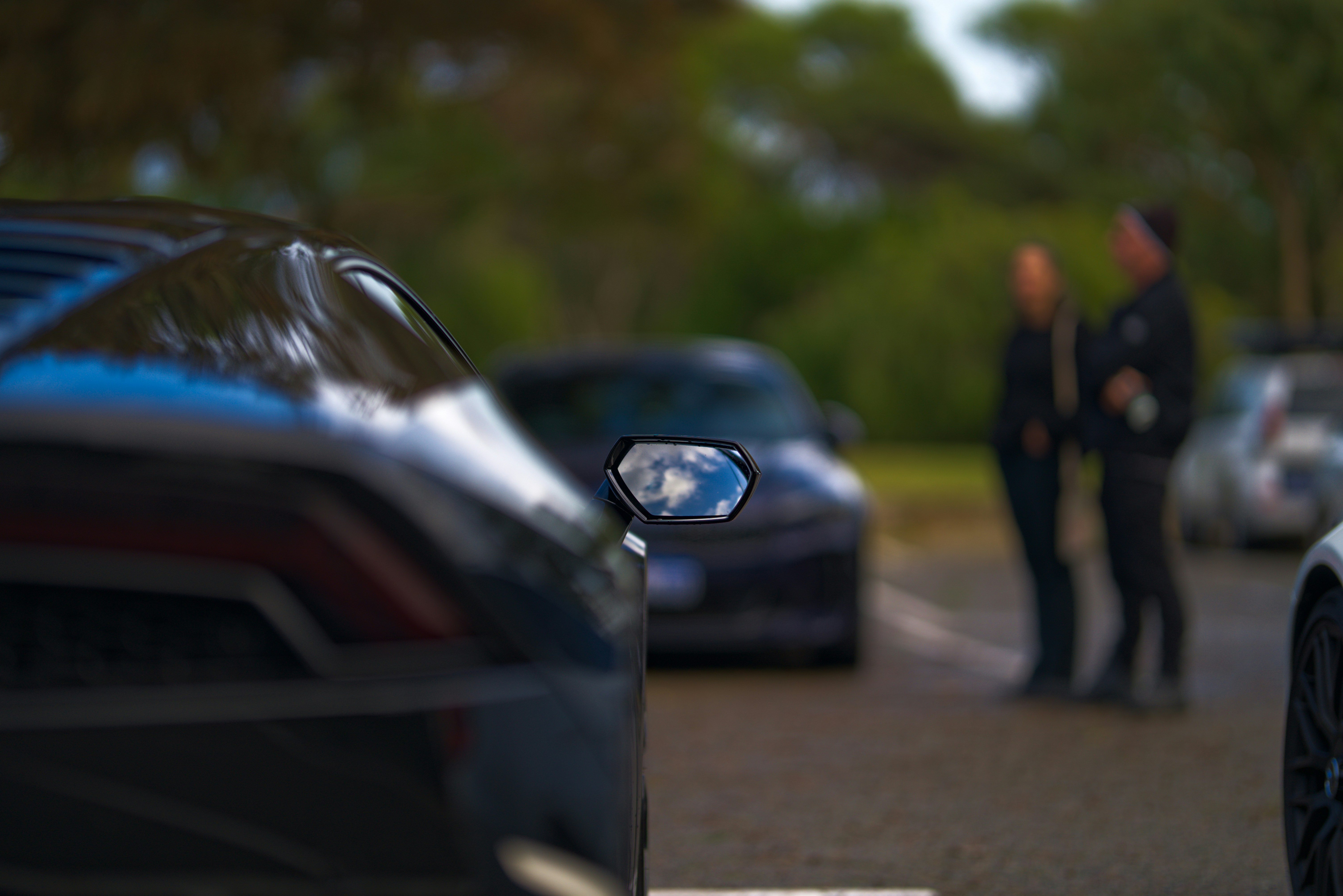 A Focused Glance: The Mirror of a Supercar Between Idle Conversations