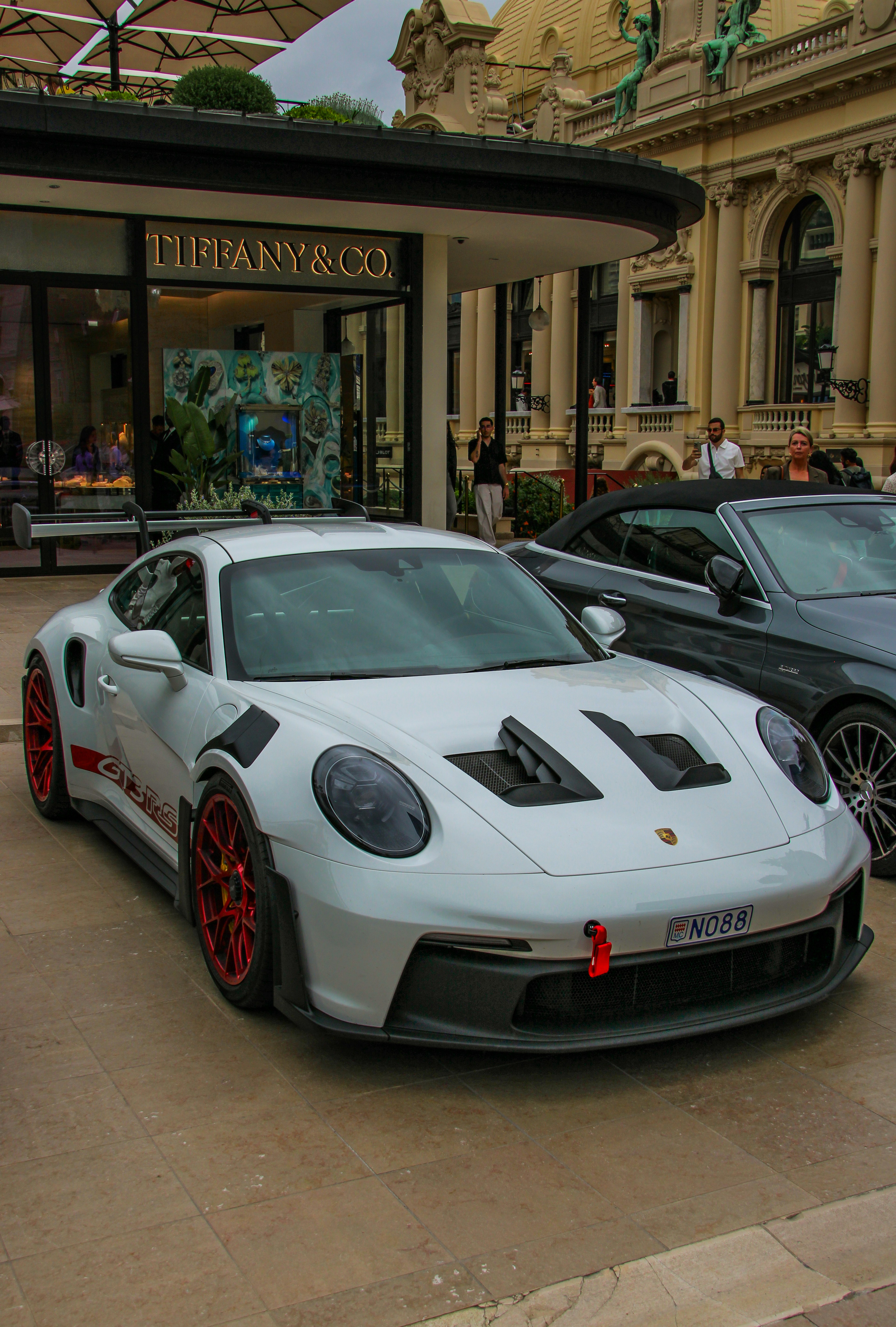 White Porsche GT parked outside Tiffany & Co. amid a European plaza backdrop