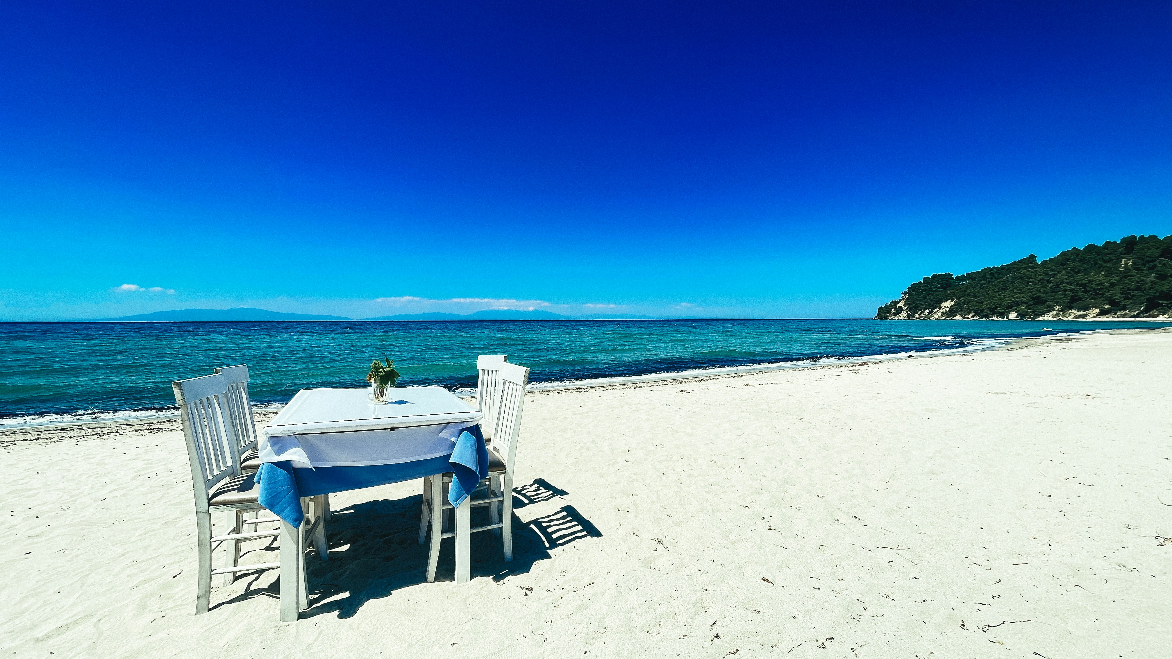 Table and chairs on a white sandy beach, blue ocean.