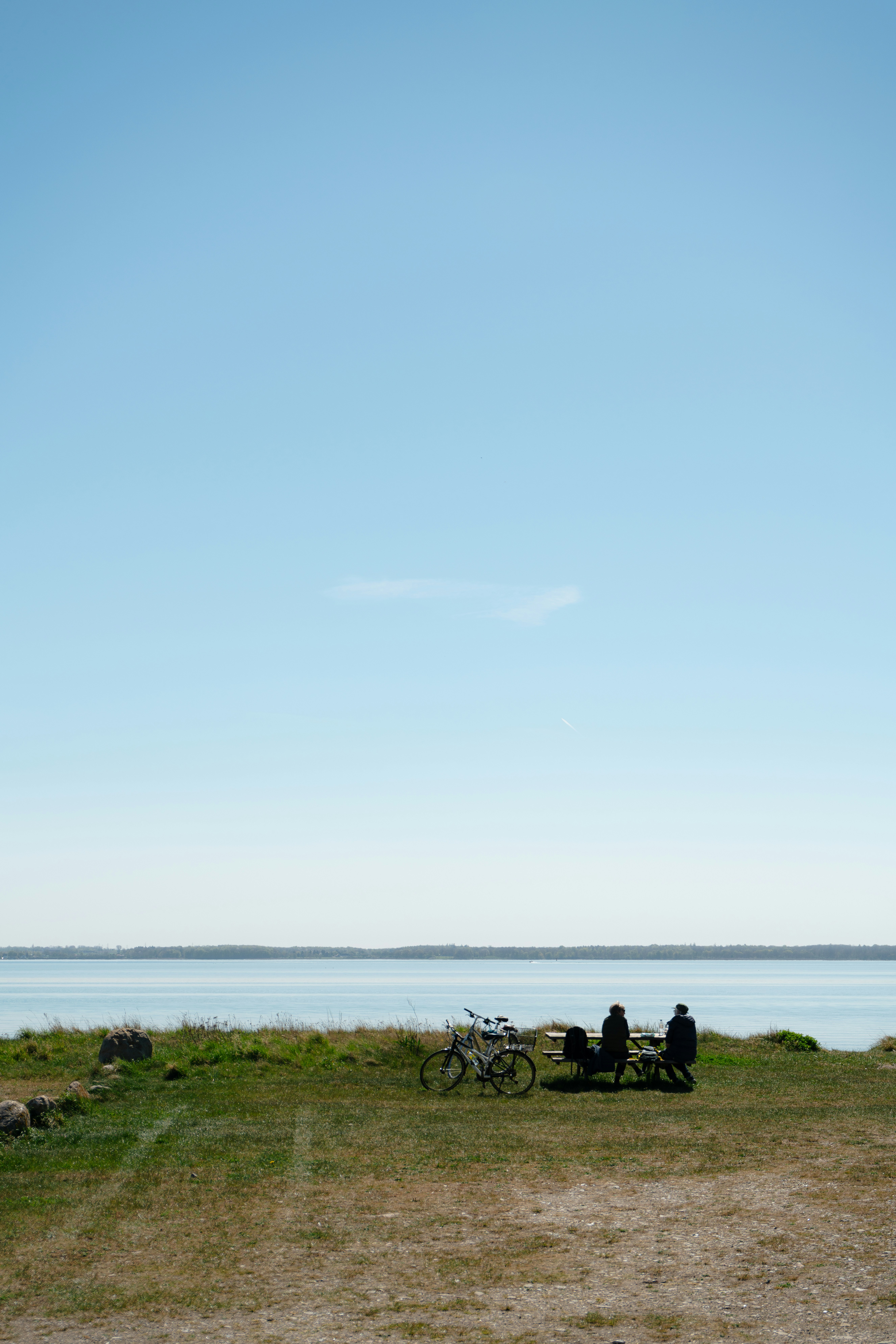 Quiet Riverside Break: Bicycles, Bench, and Silhouettes under a Wide Sky