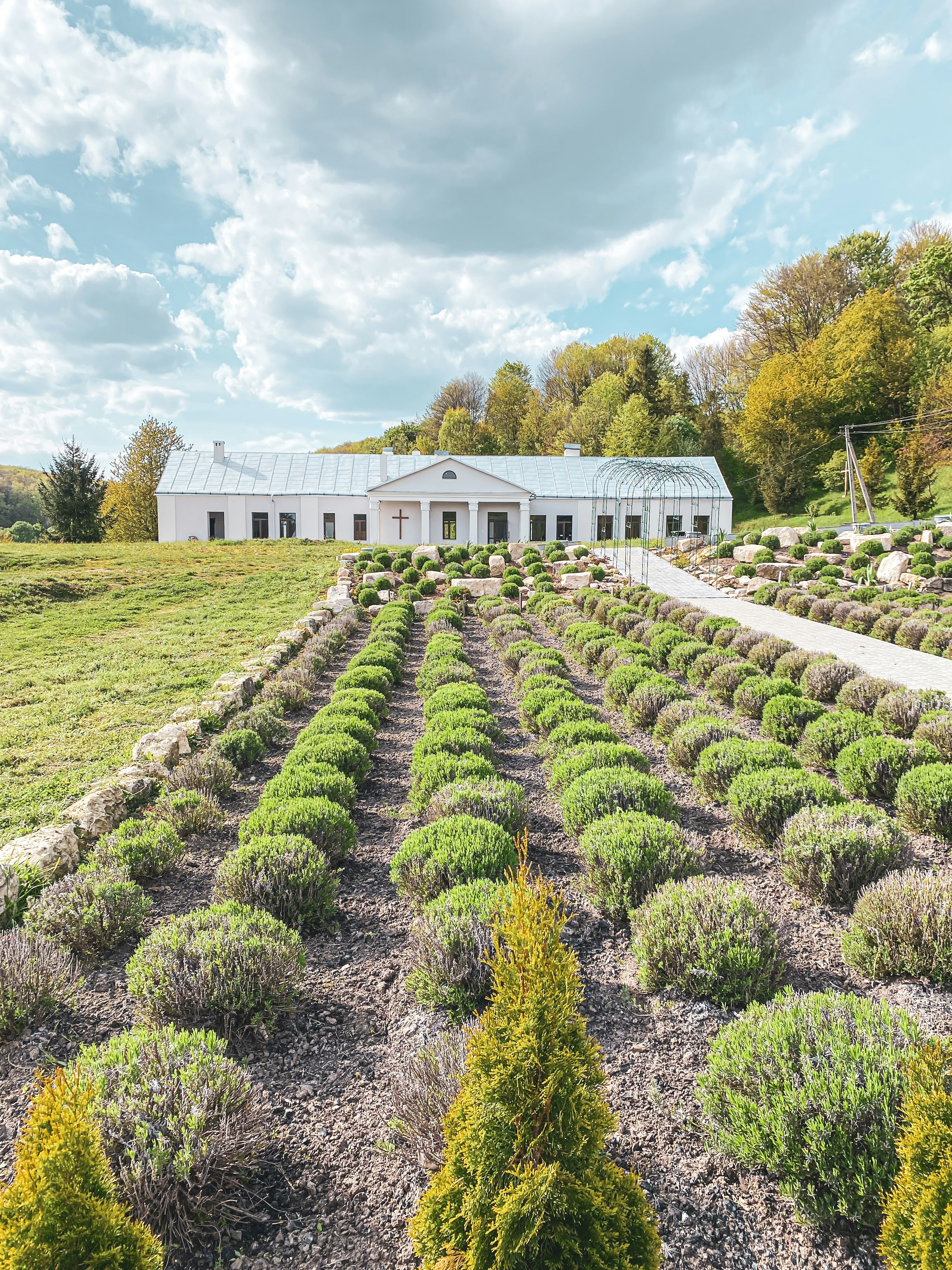 Symmetrical garden rows lead to a white institutional building under a bright sky