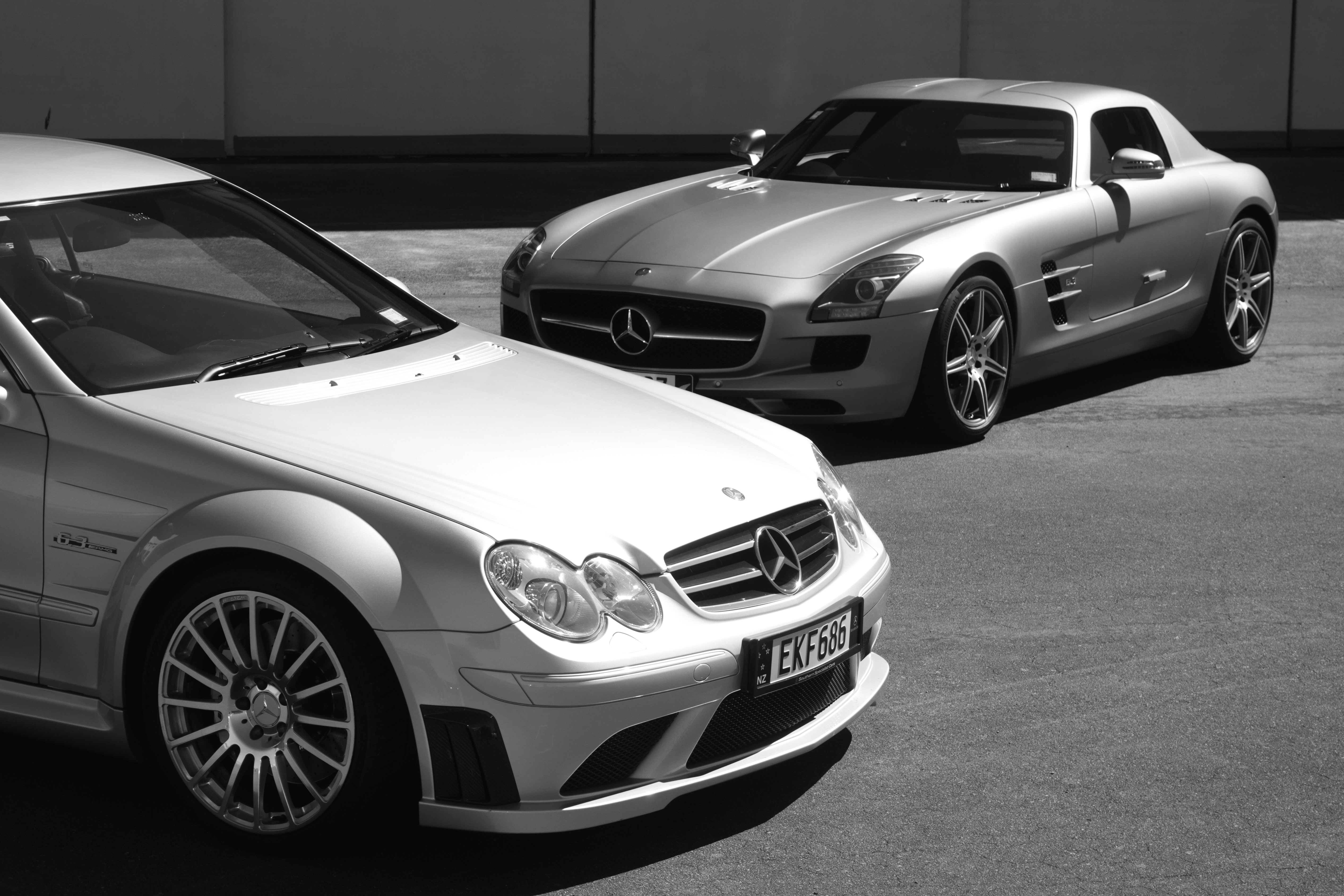 Two mercedes-benz cars parked on pavement in black and white.