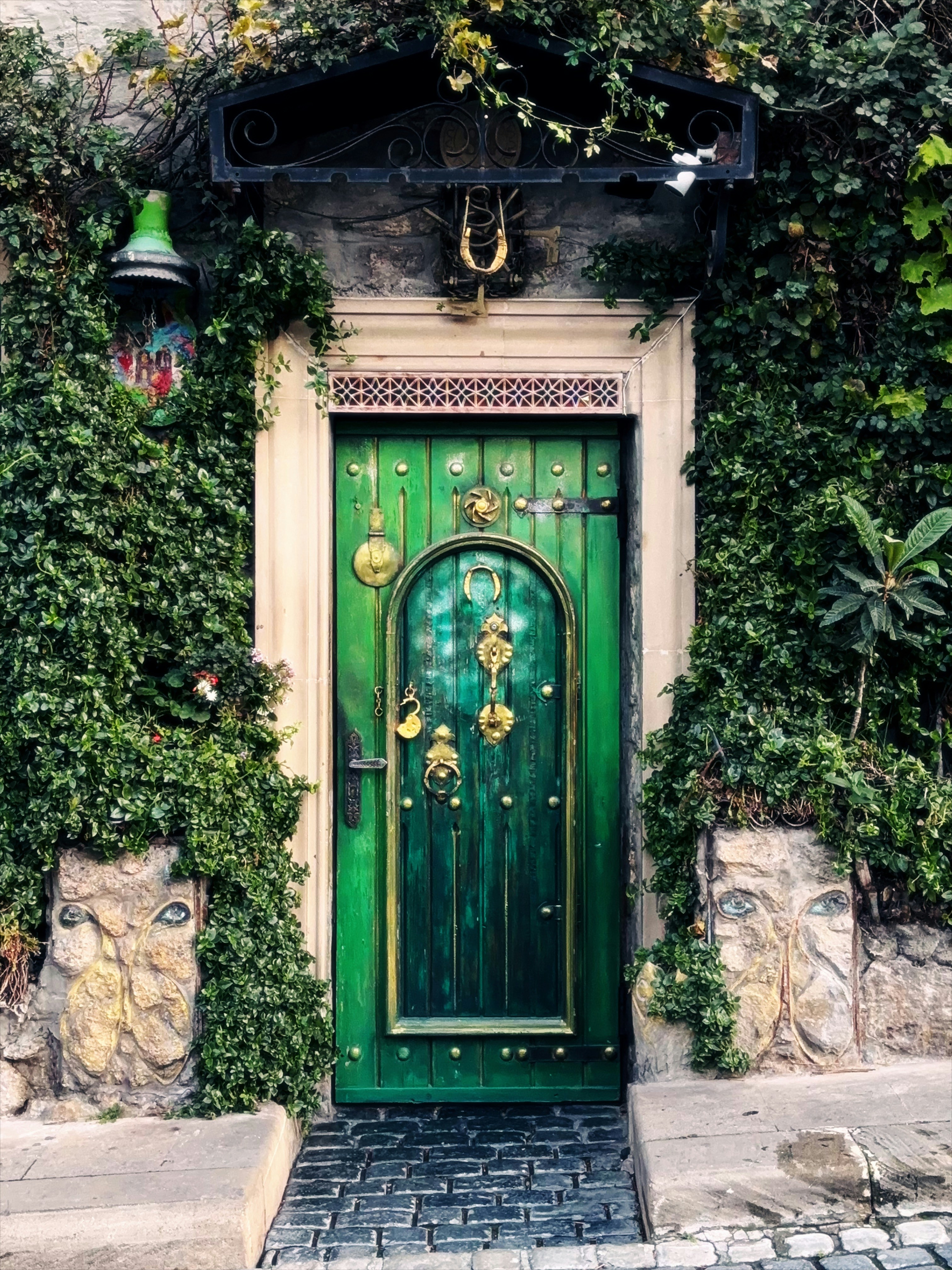 Verdant Portal: A Green Carved Door Framed by Ivy and Stone Faces