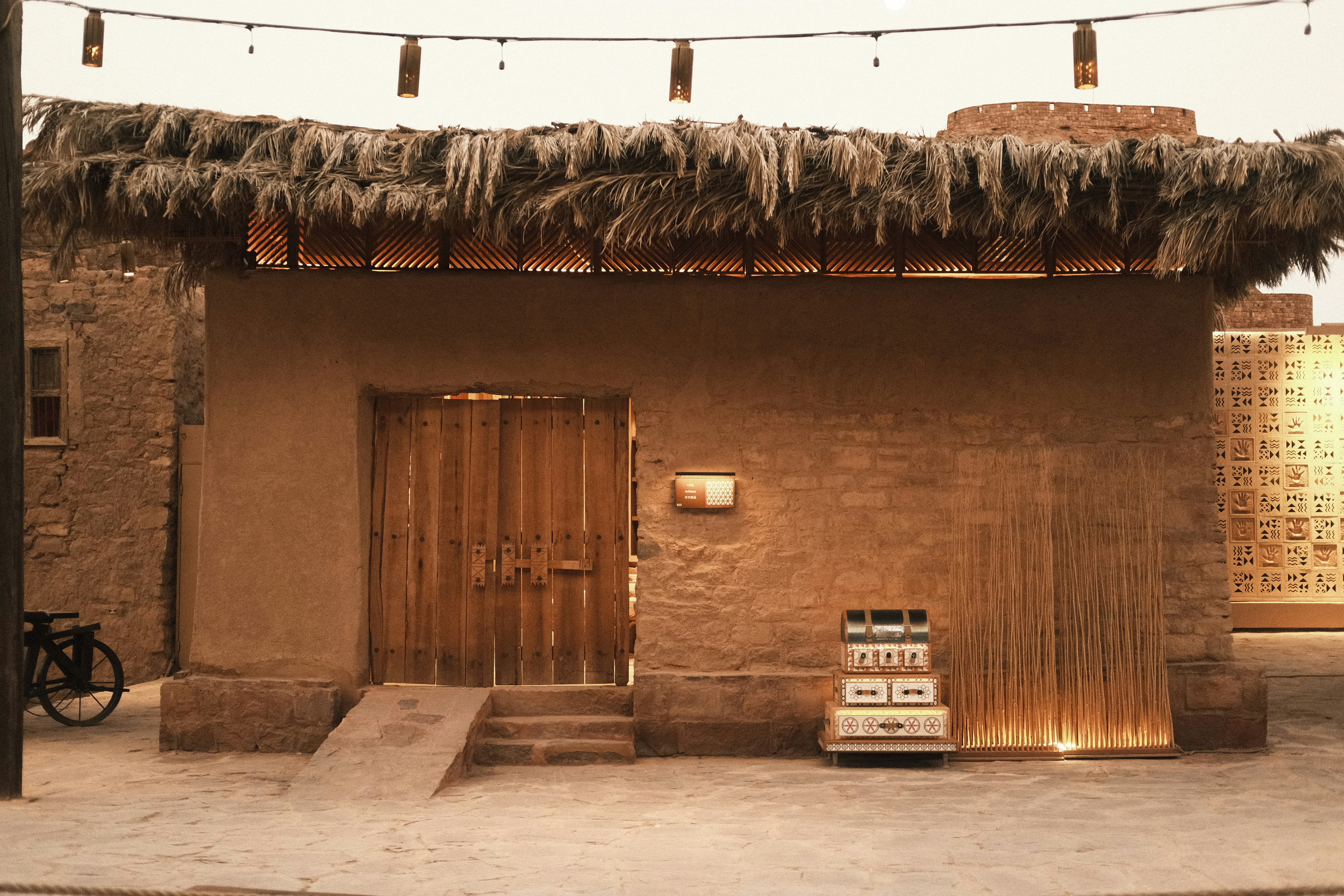 Adobe building with thatched roof, wooden door, and string lights.