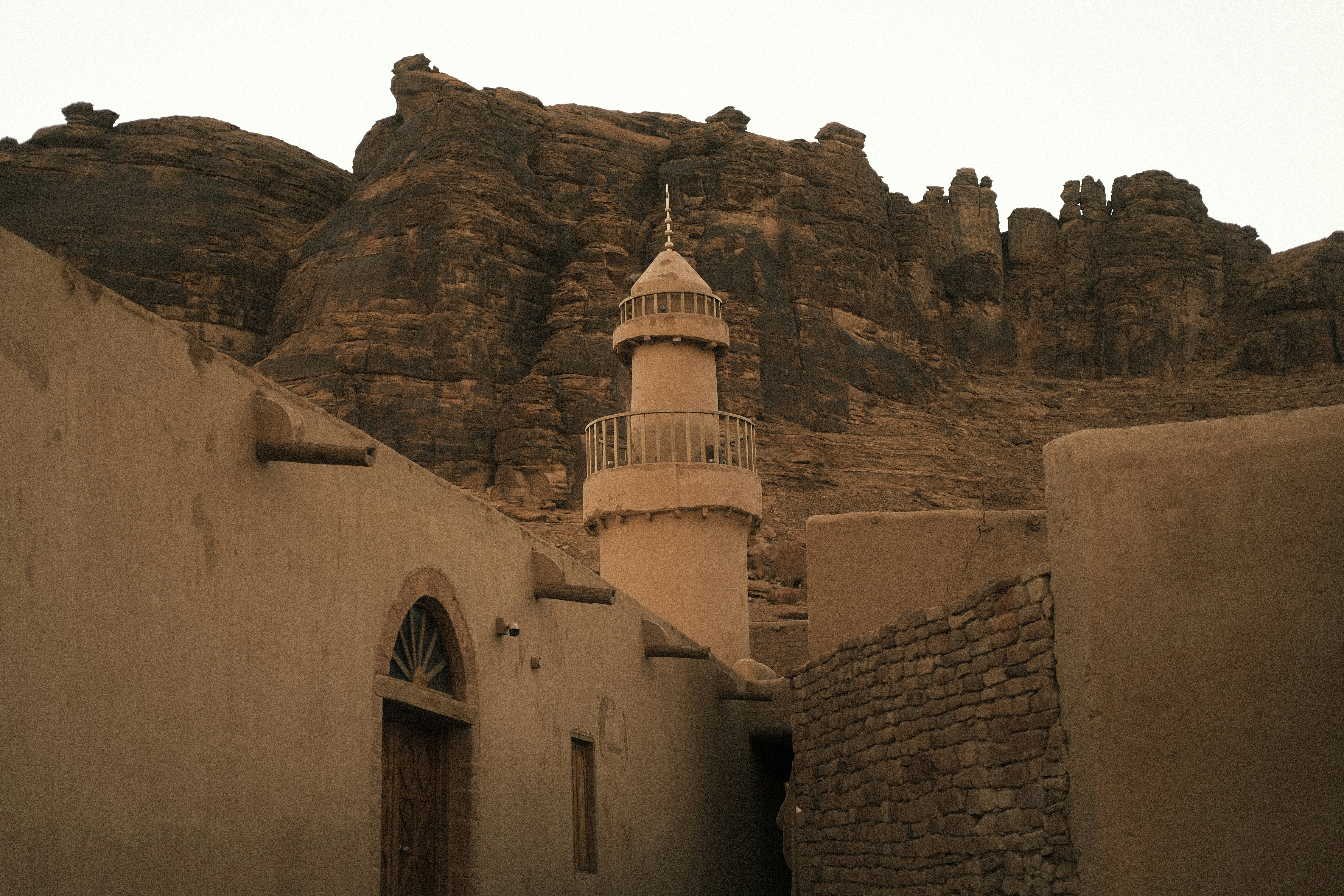 Ancient minaret amidst desert mountains and traditional mud-brick buildings.