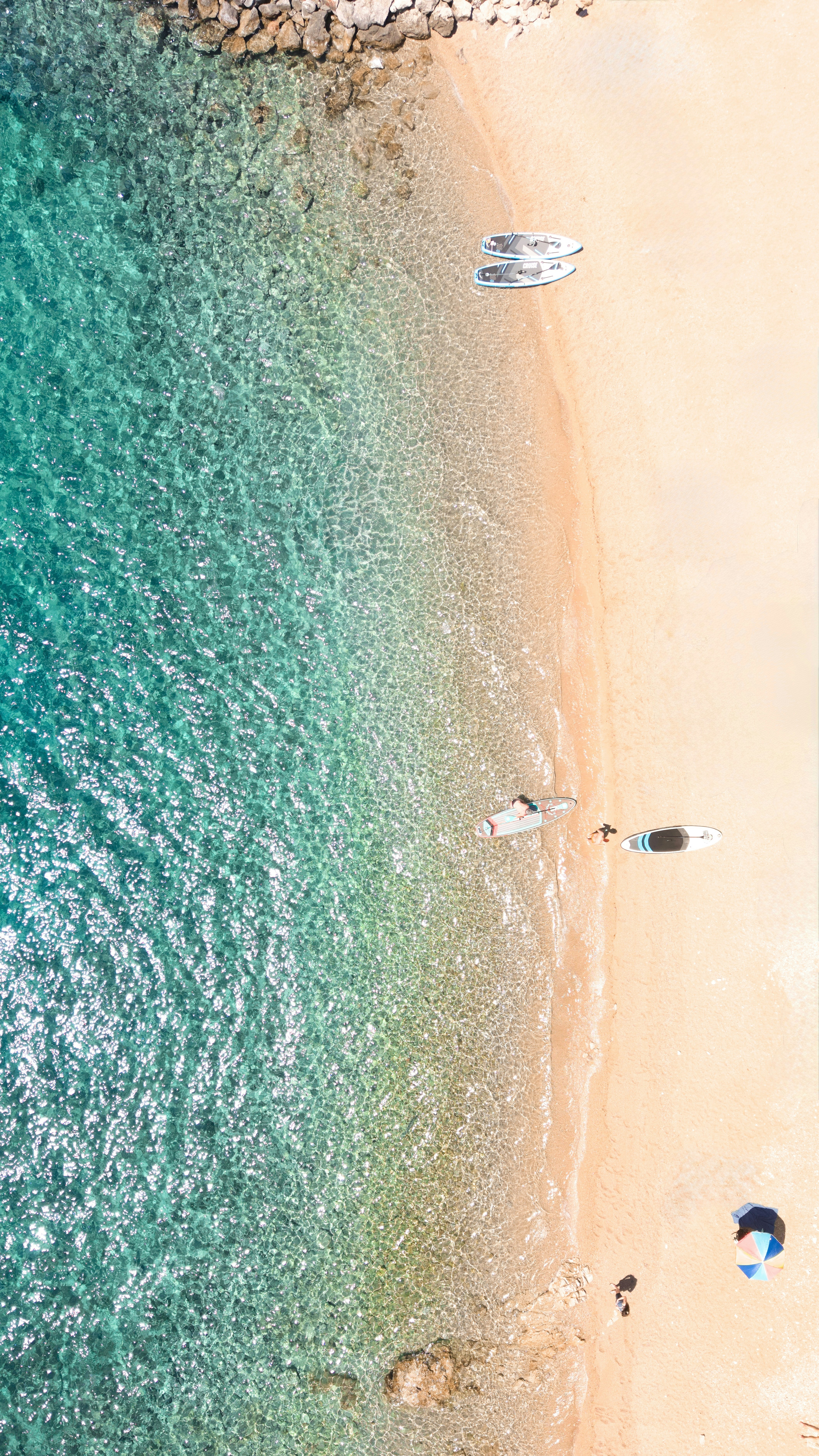 Clear turquoise water meets sandy beach with paddleboards.