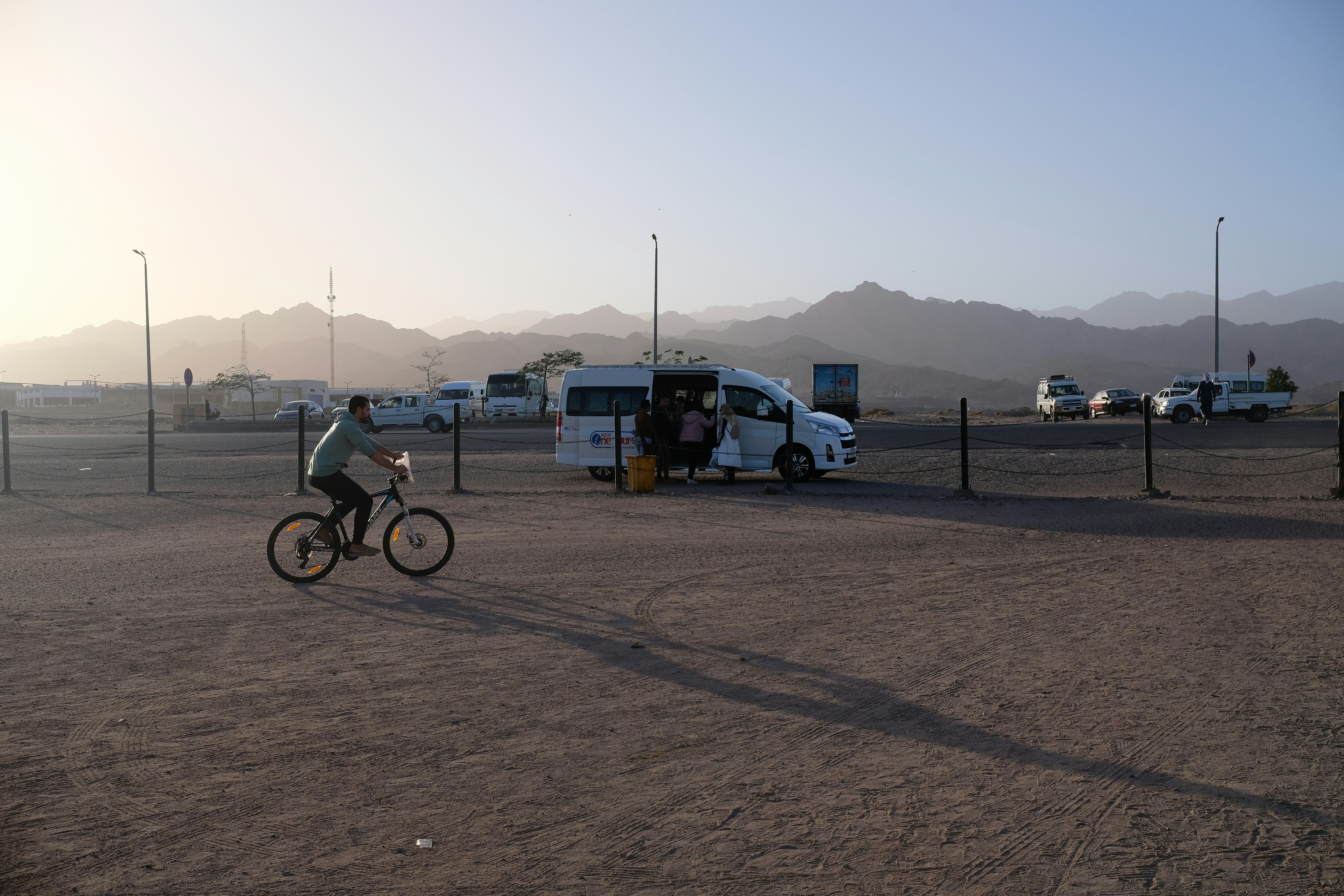 Desert Wake: A lone cyclist drifts past a mobile food van under distant mountain silhouettes
