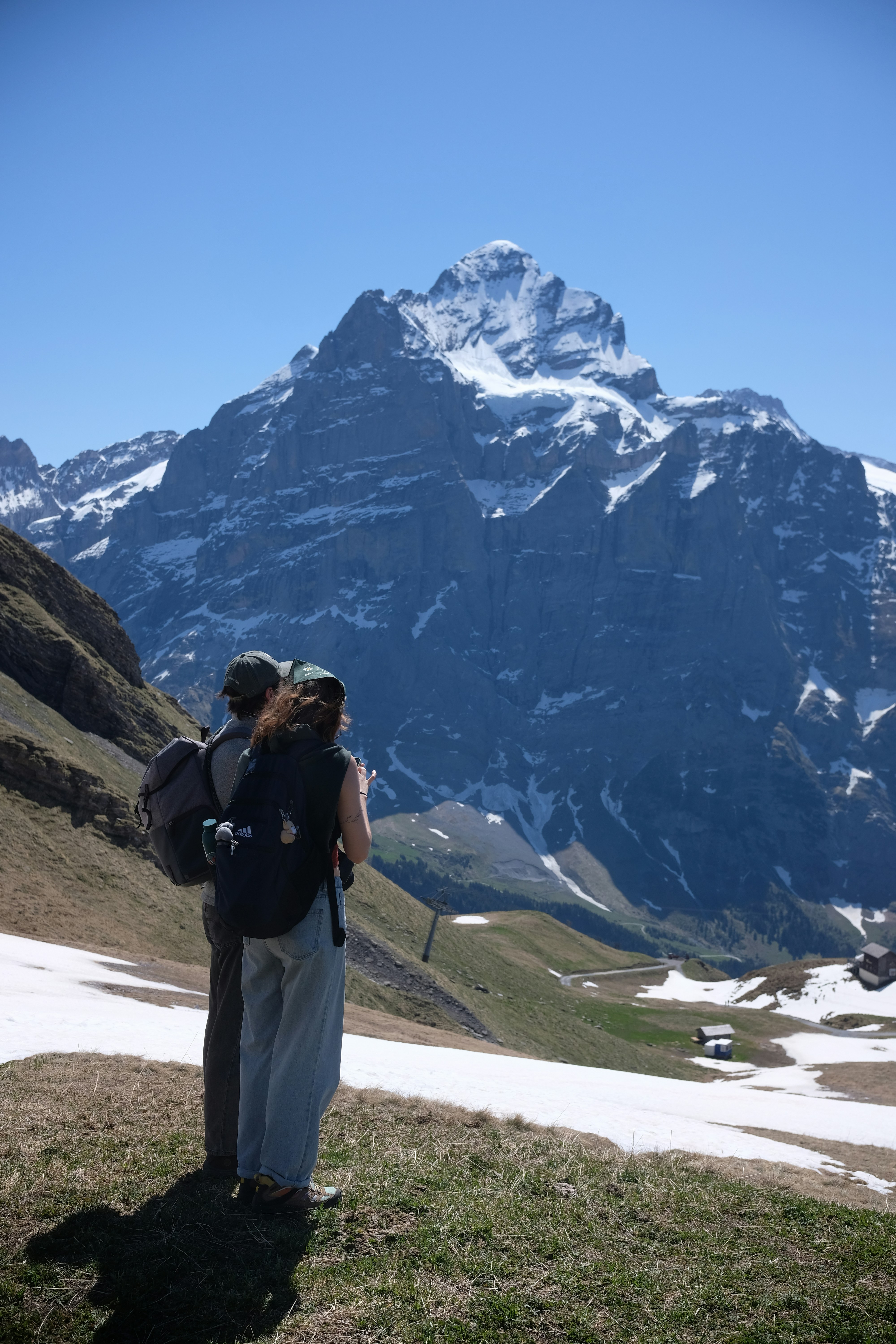Two hikers at the base of a colossal glacier-crowned peak