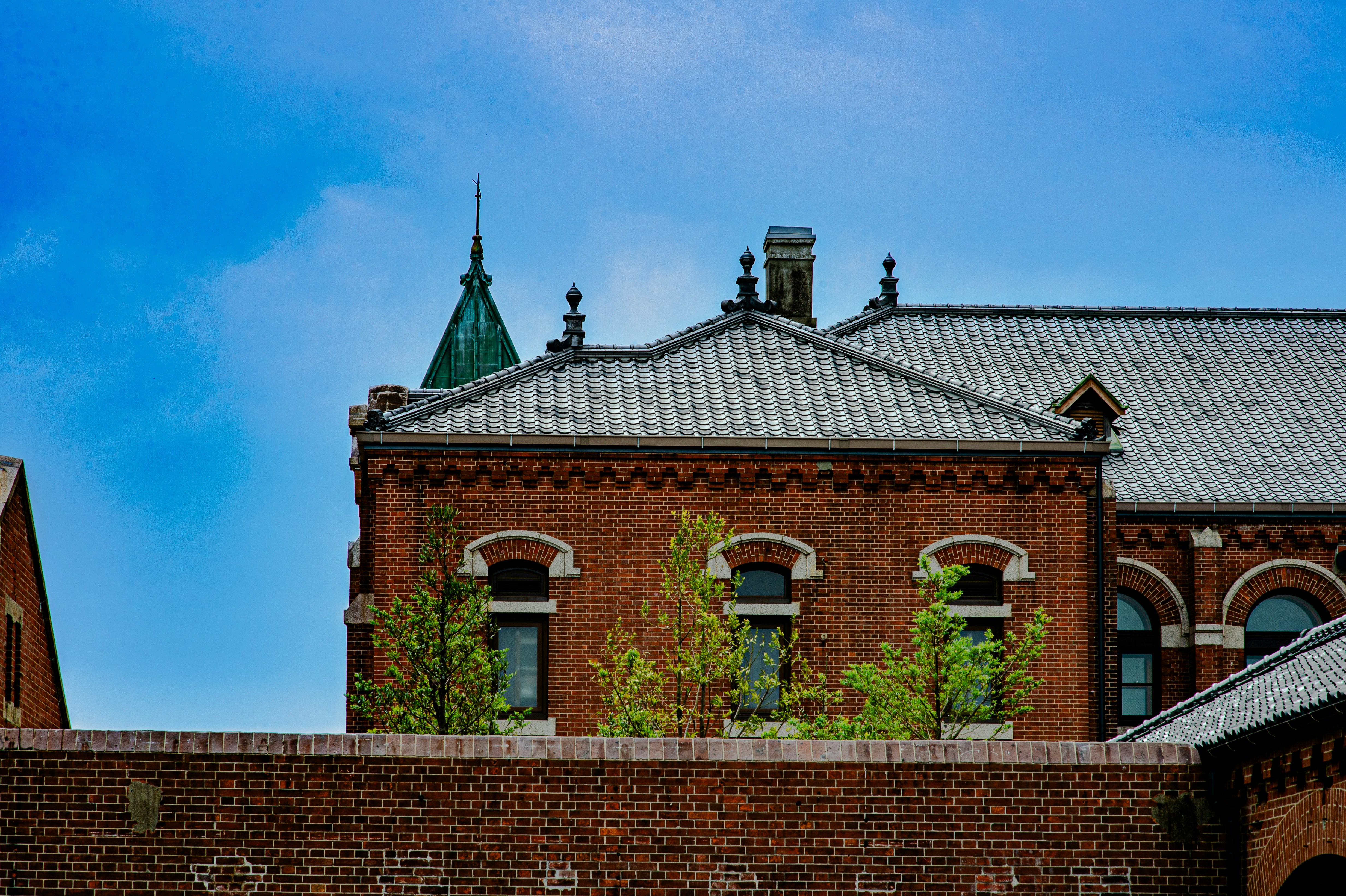 Brick building with tiled roof, green spire, and blue sky.