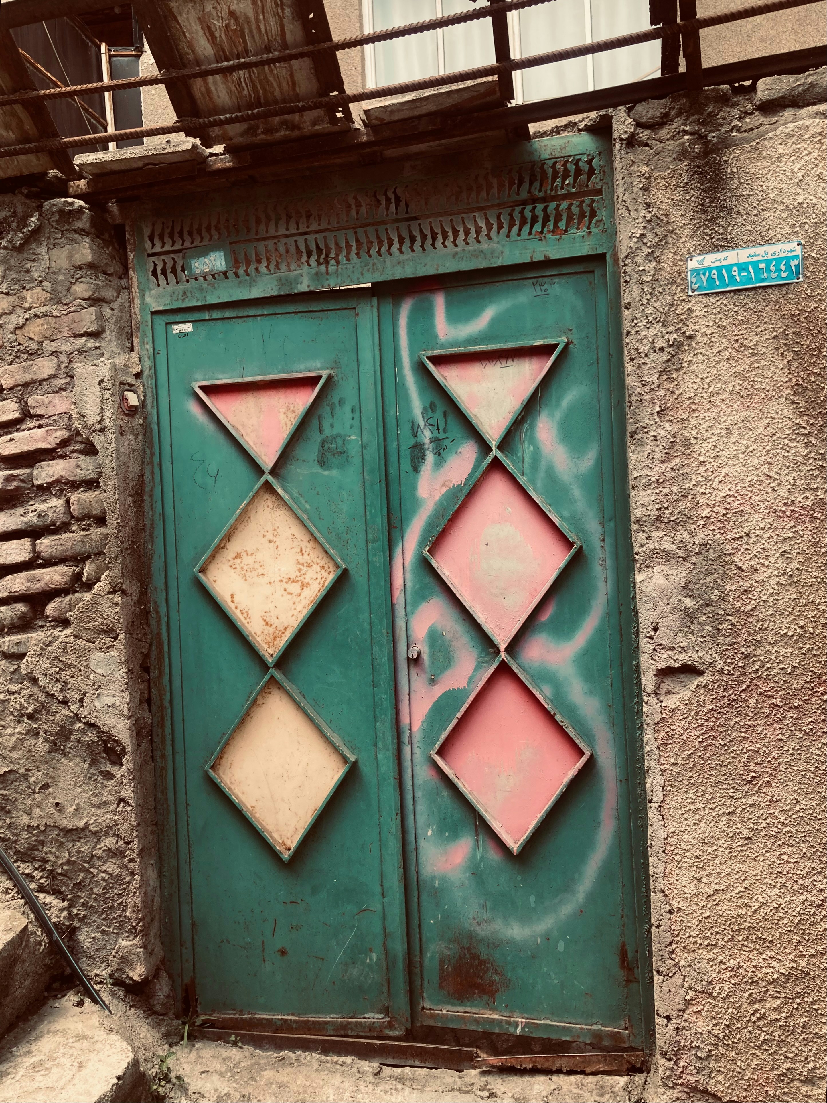 Weathered turquoise door with diamond panels in a sun-baked alley