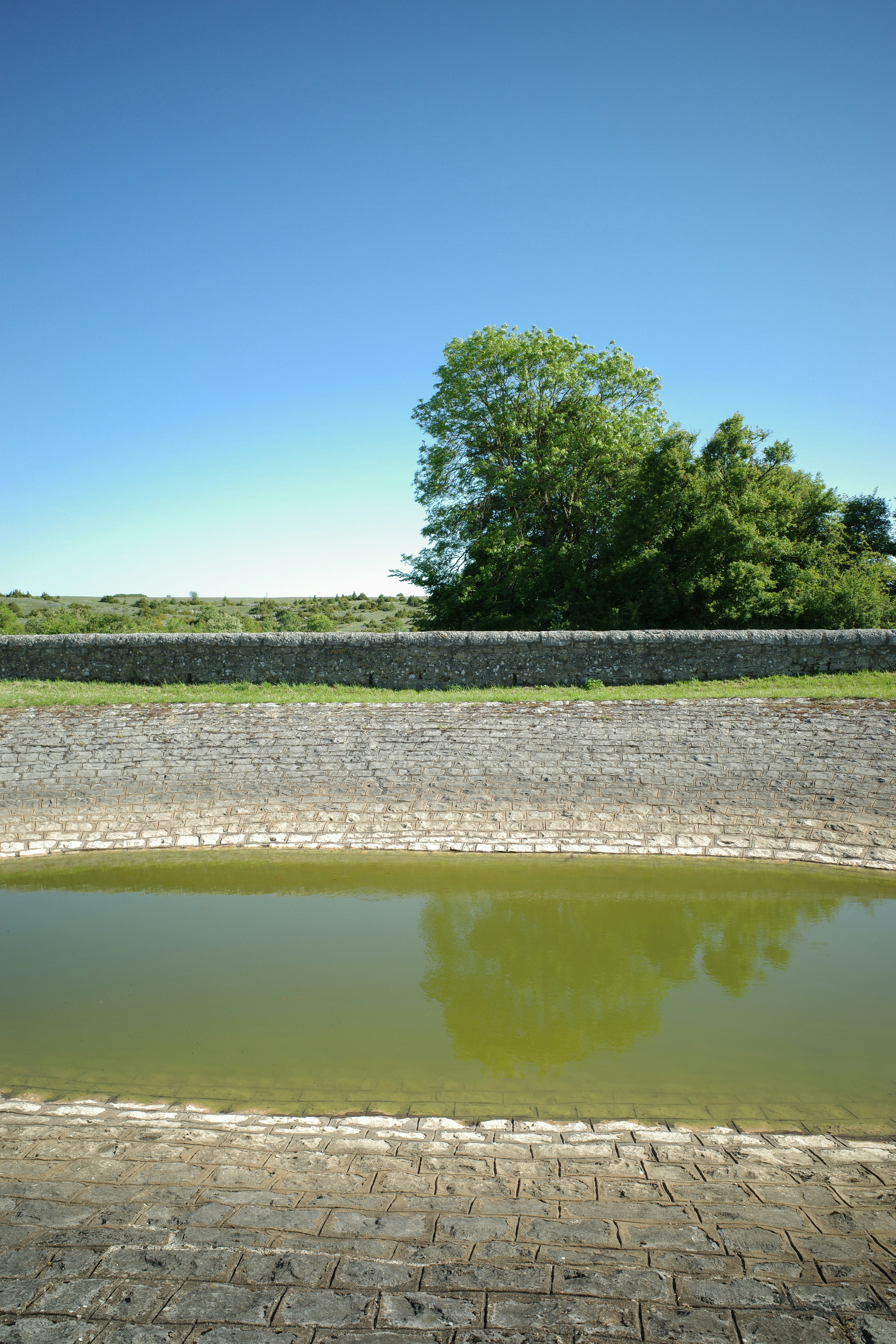Stone Wall Echoes Over a Quiet Pool Under a Wide Blue Sky